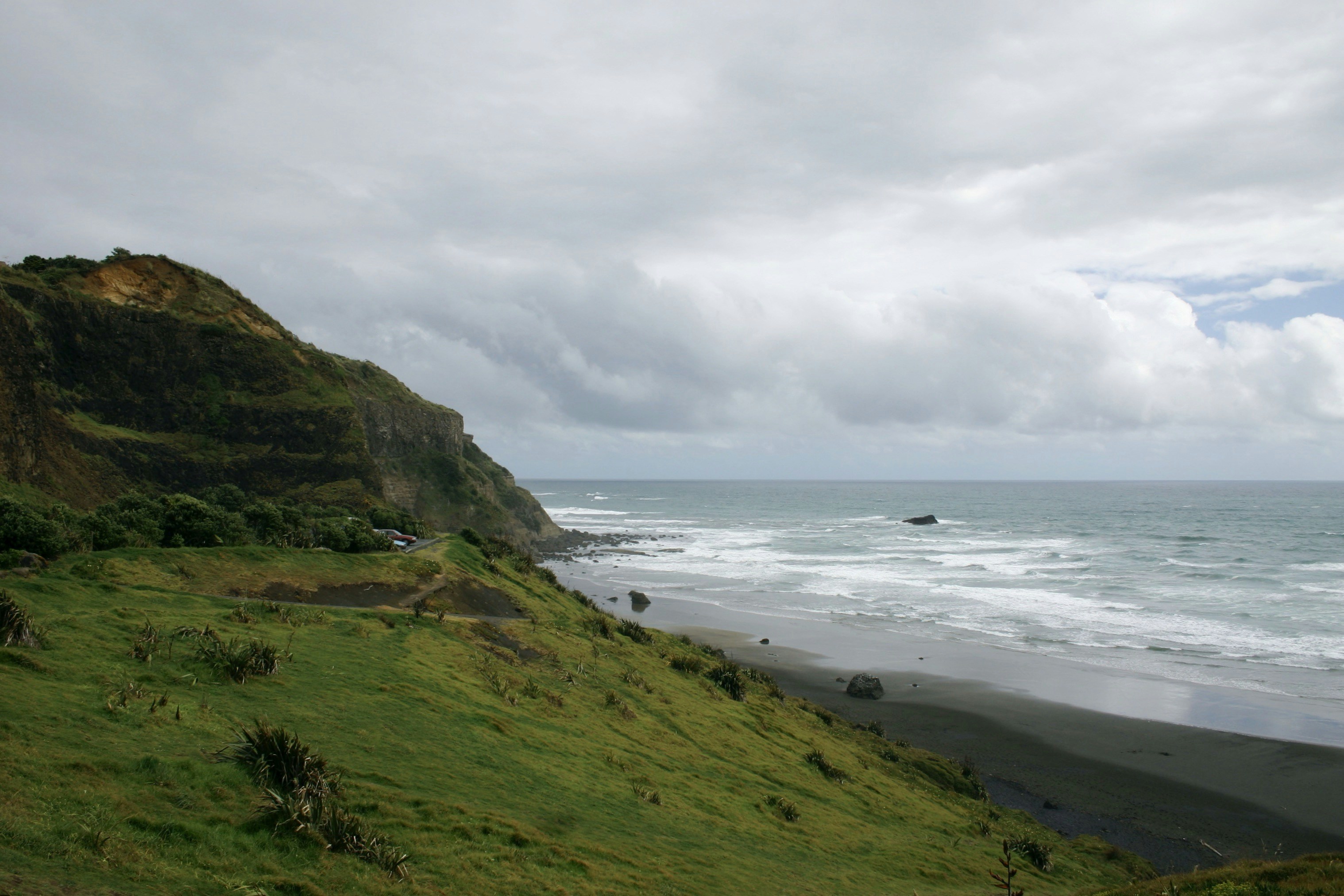 Lush green hillside meeting a rugged coastline under a cloudy sky.