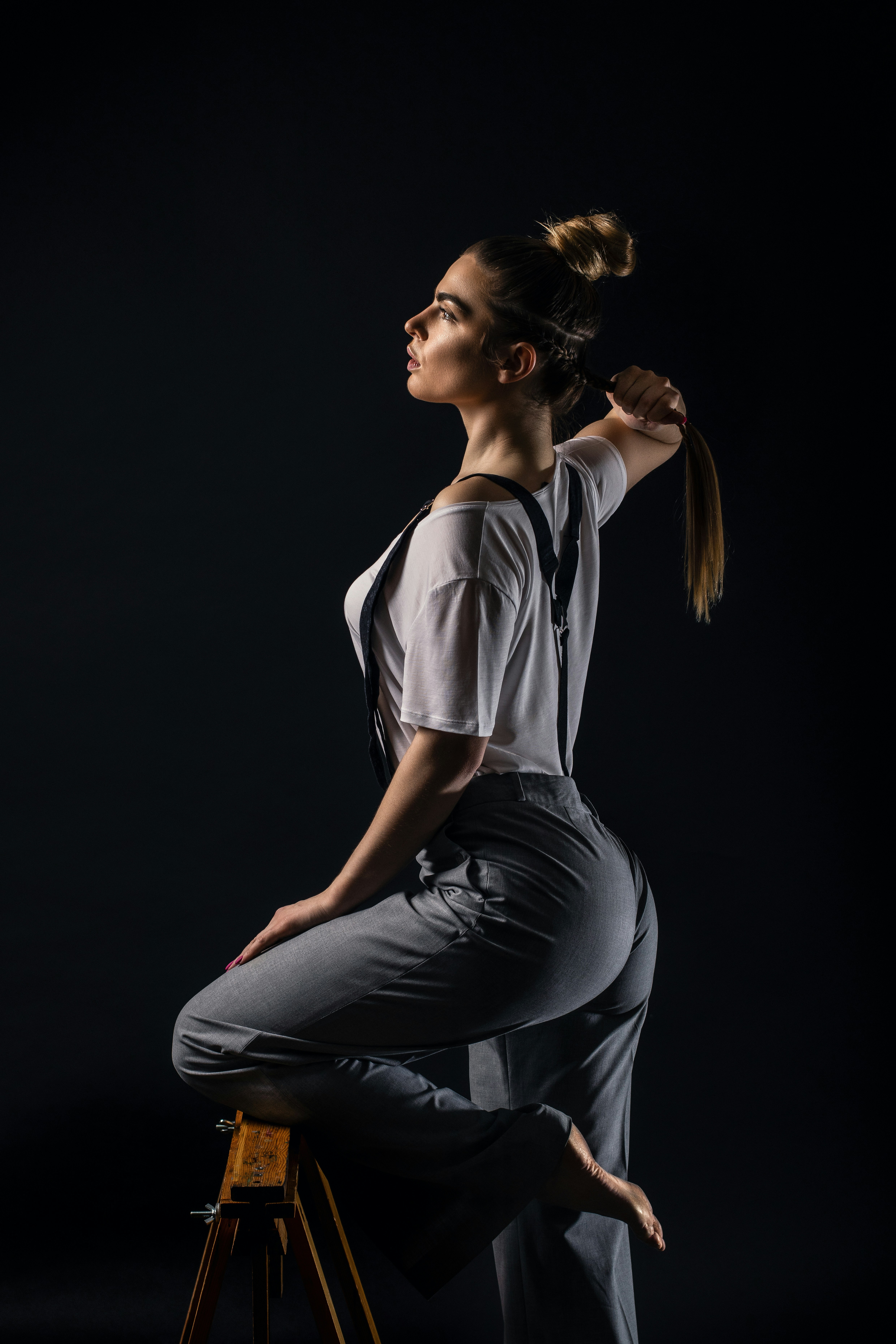 Female model striking a dynamic pose on a stool, showcasing a blend of strength and grace against a dark backdrop.