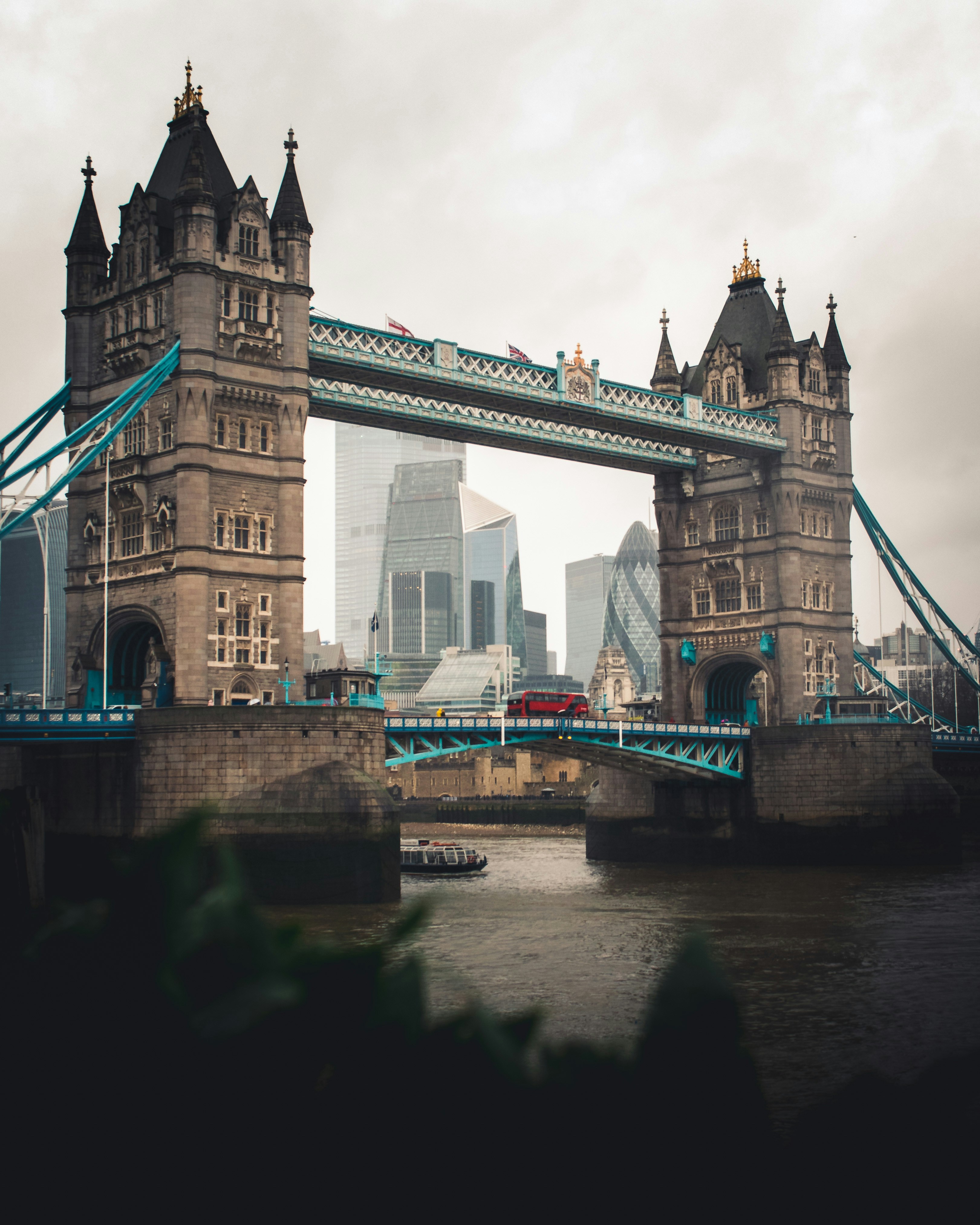 Tower Bridge stands majestically over the River Thames, framed by modern skyscrapers in the background. The scene captures a blend of historical architecture and contemporary city life.
