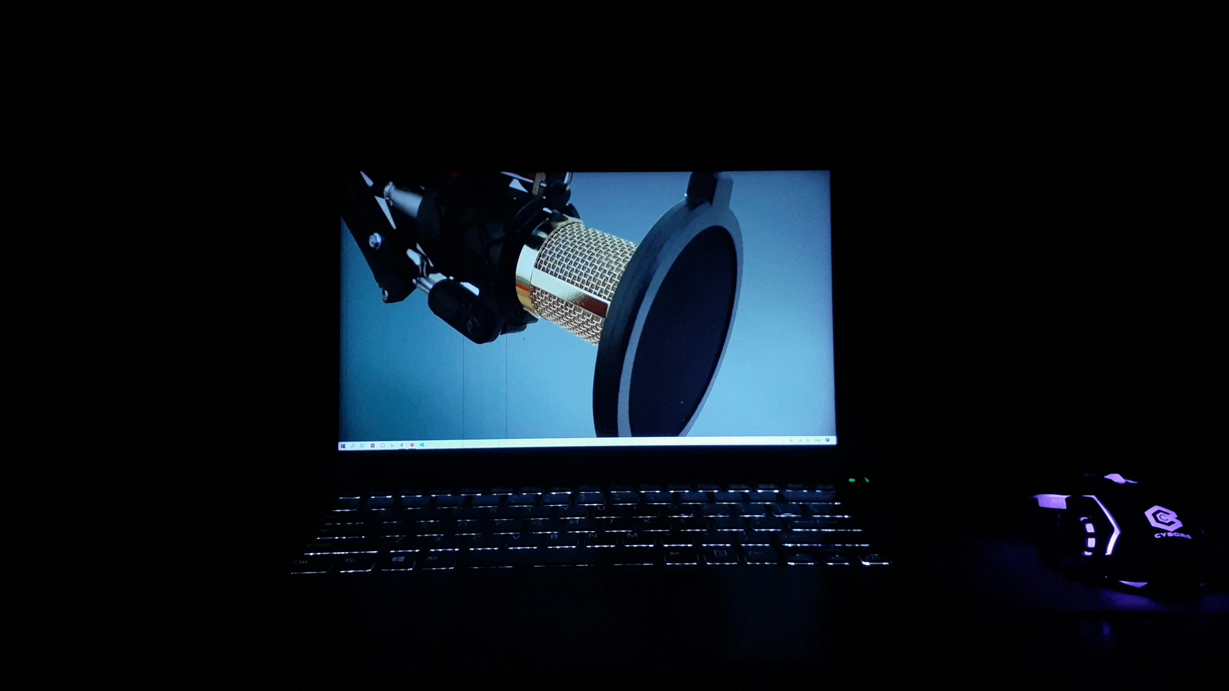 Laptop screen displaying a microphone in dim lighting with a glowing mouse nearby.