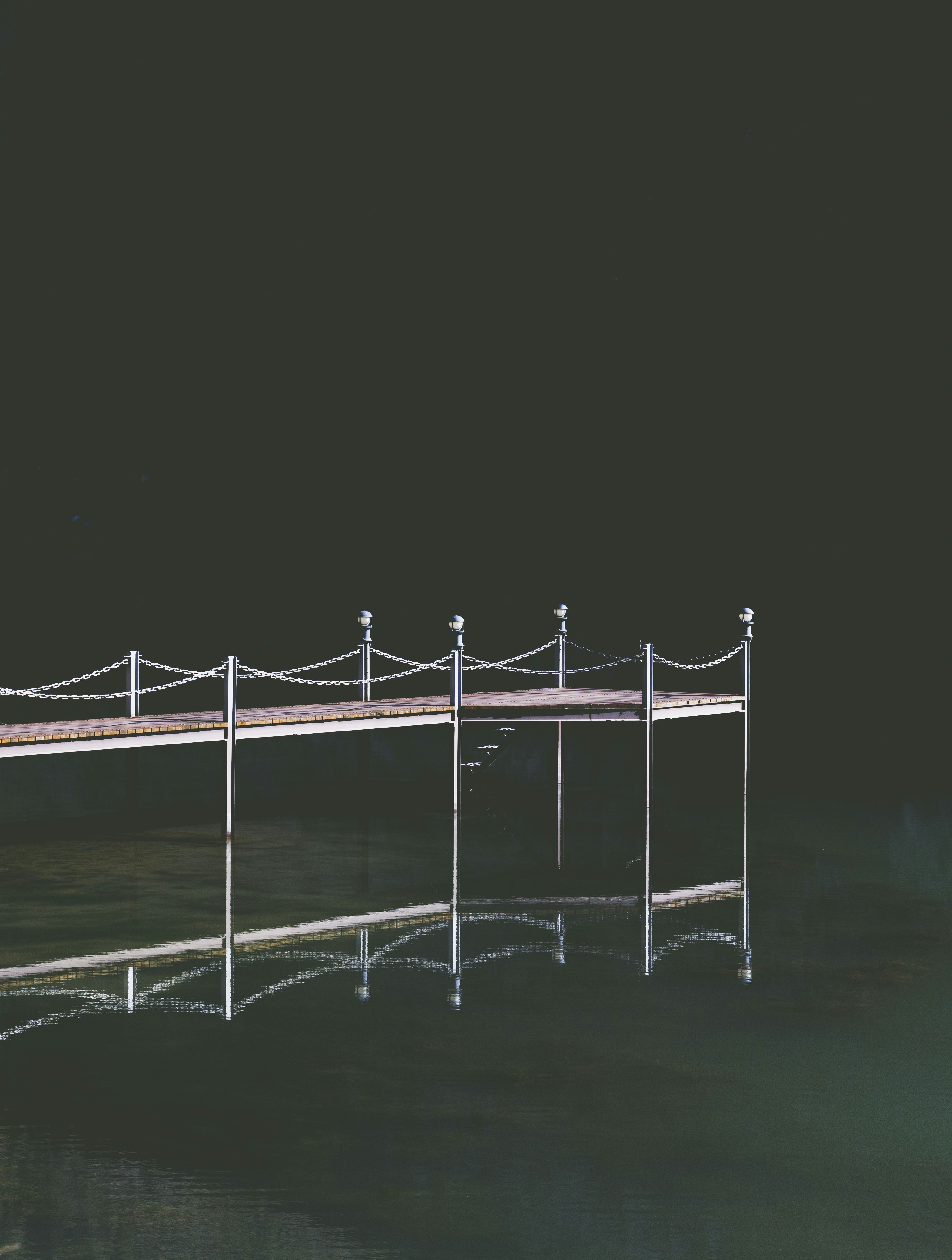 Wooden dock extending over calm waters, surrounded by dark foliage. The reflection creates a tranquil symmetry.