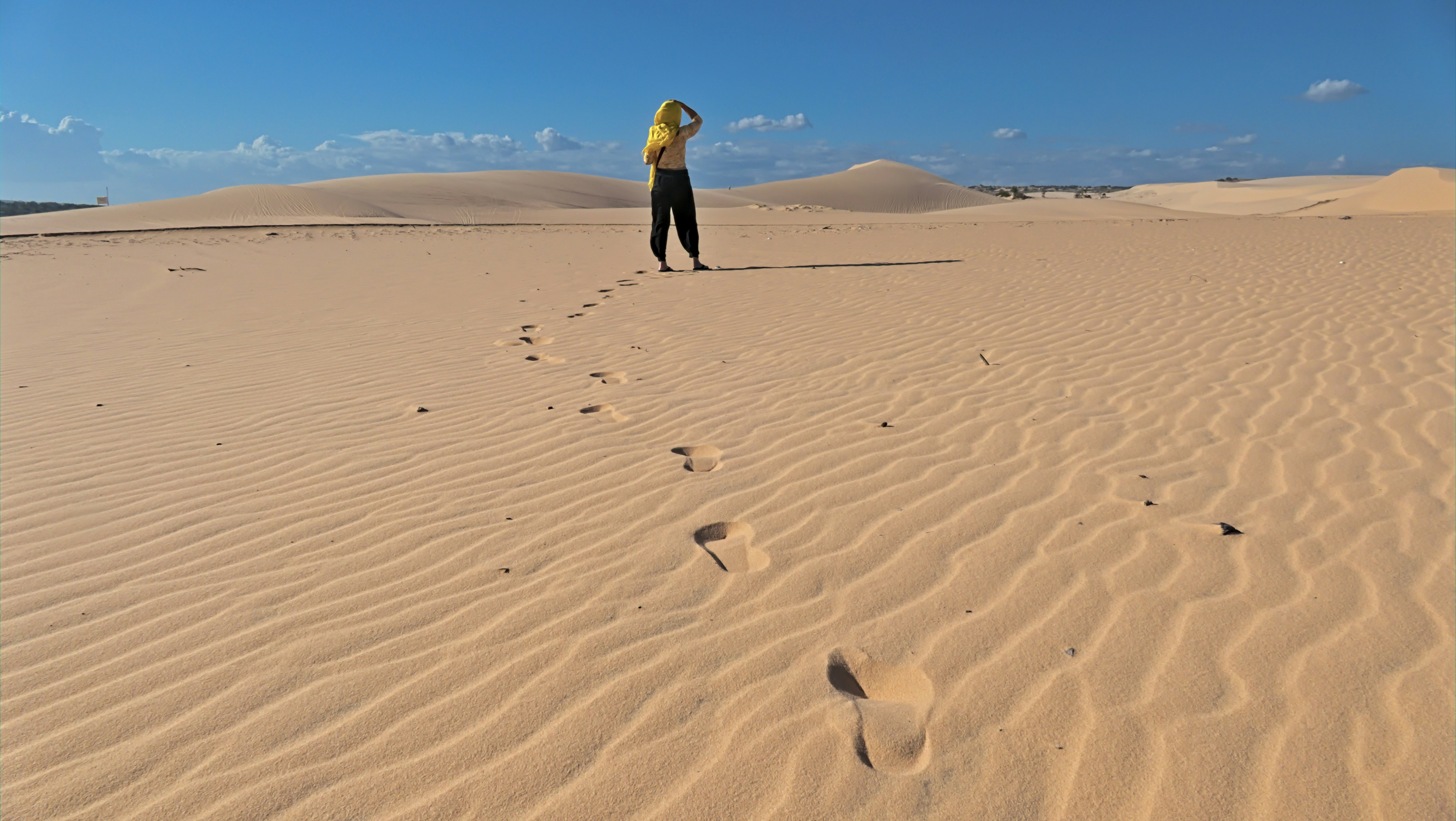 Person walking along rippled sand dunes under a clear blue sky.