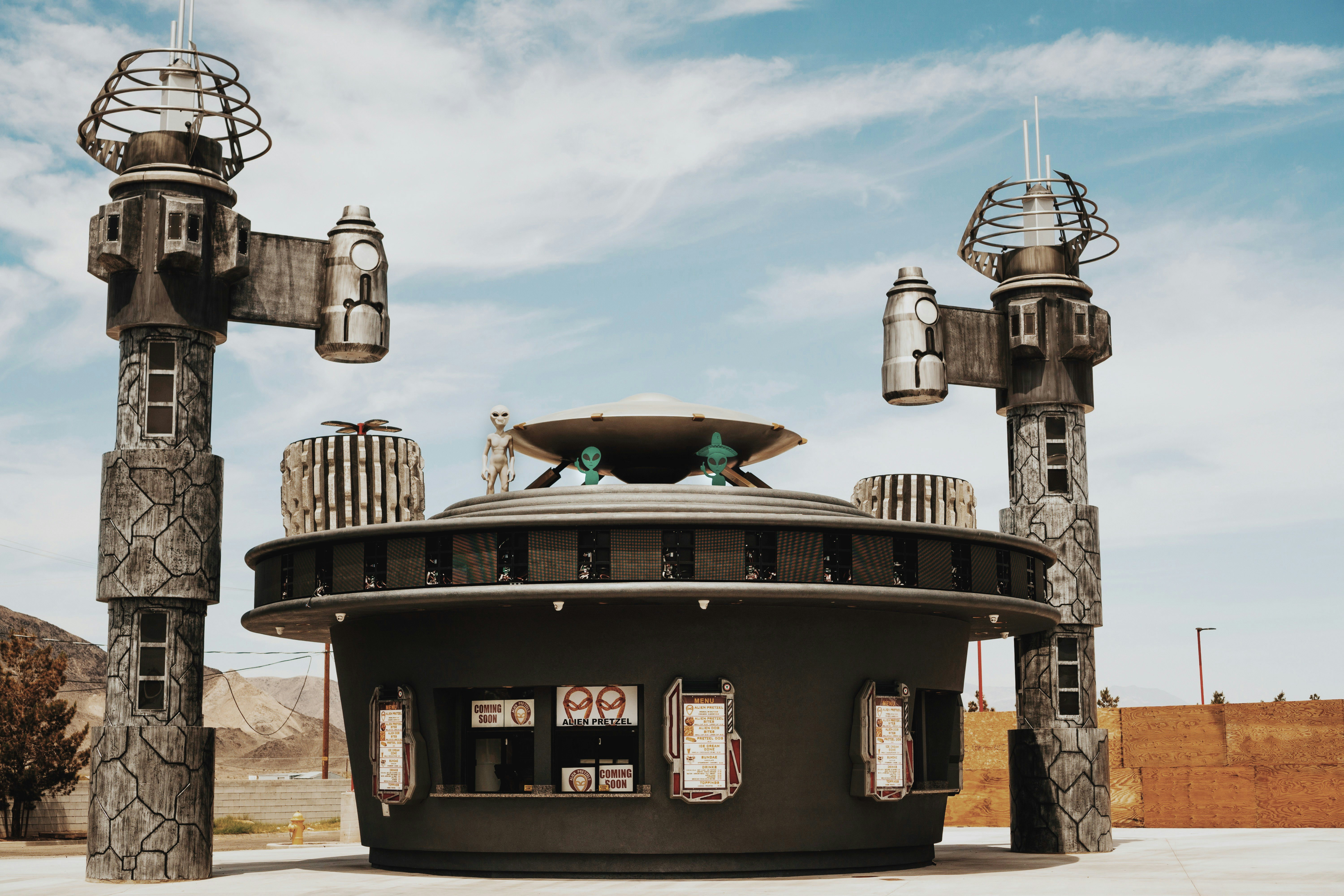 A quirky roadside attraction featuring a UFO-shaped structure with alien figures, surrounded by towering, industrial-style towers. The unique design invites curiosity and exploration.