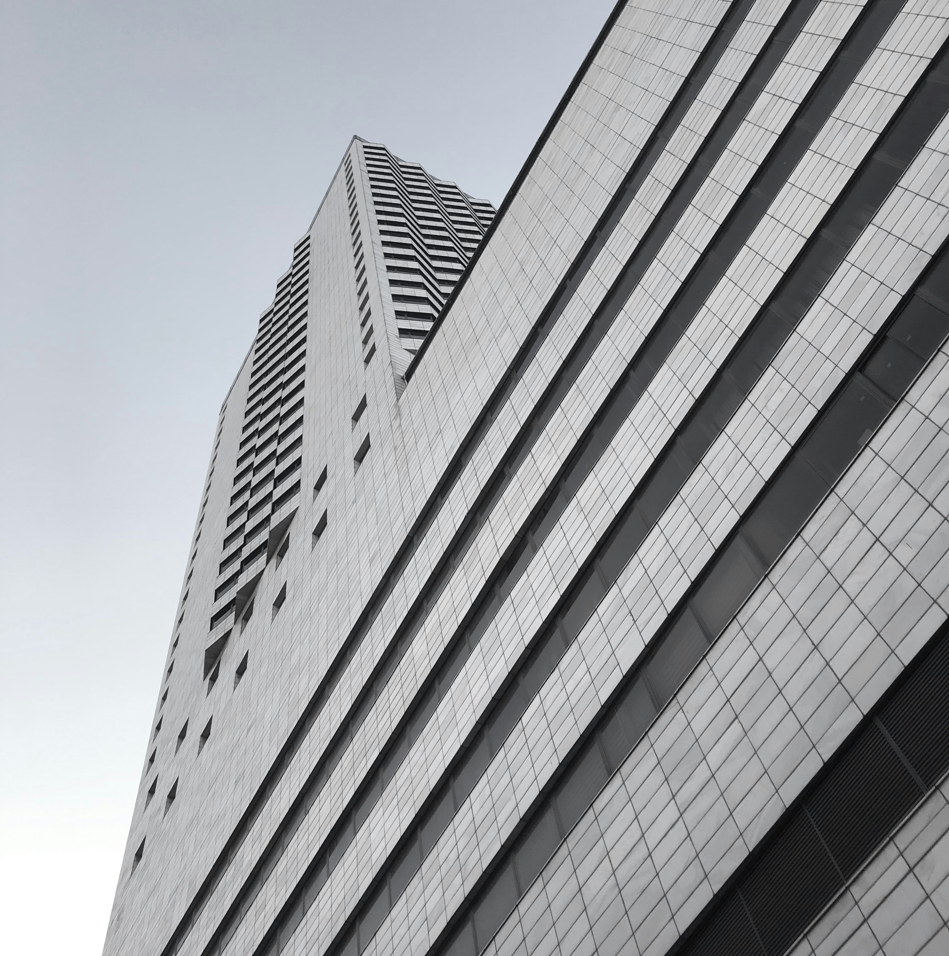 A modern architectural structure captured from a low angle, emphasizing its towering height and geometric patterns. The monochromatic tones enhance the building's sleek design.