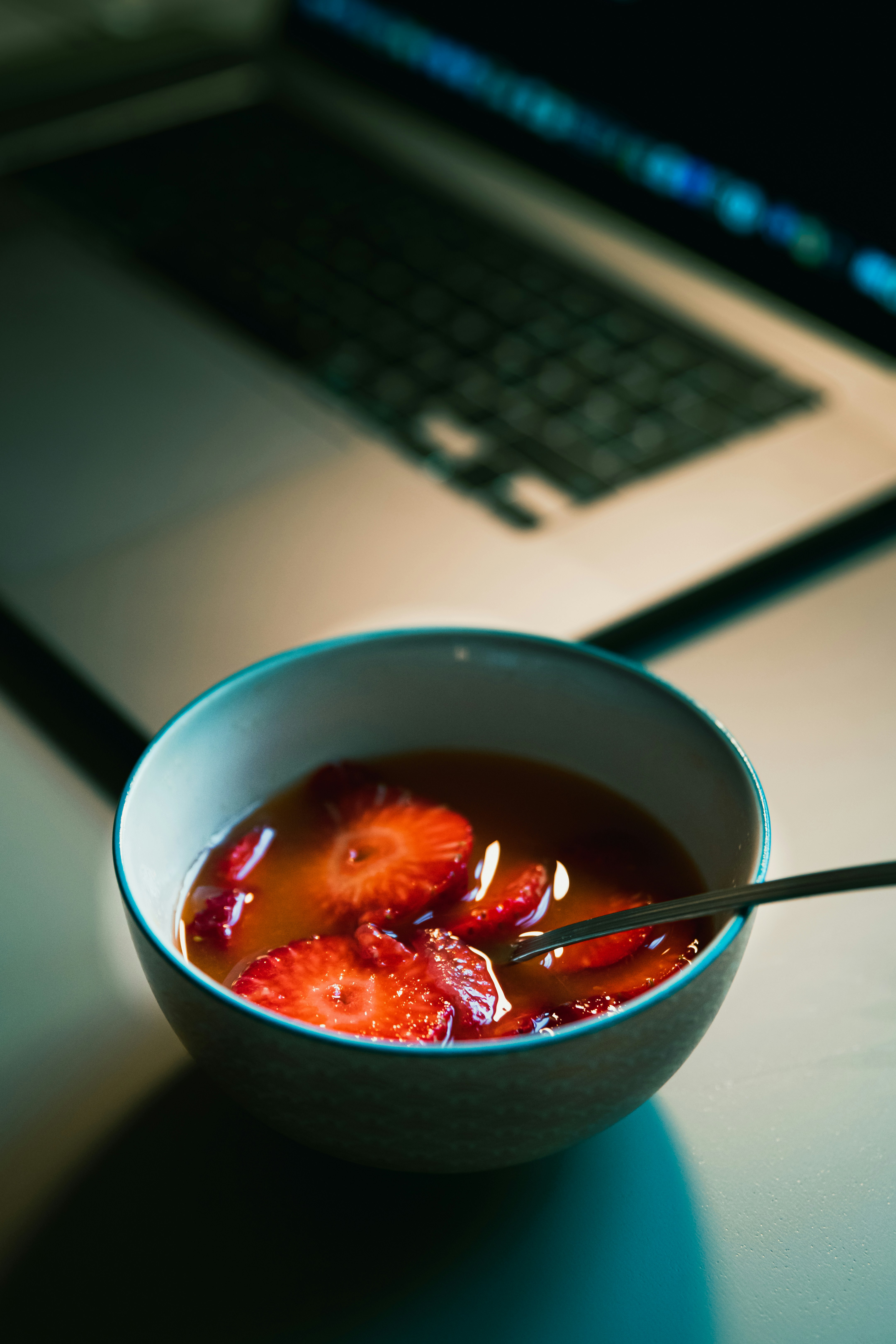 Crimson Strawberries in a Teal Bowl: A Quiet Desk Still-Life with Laptop Blur