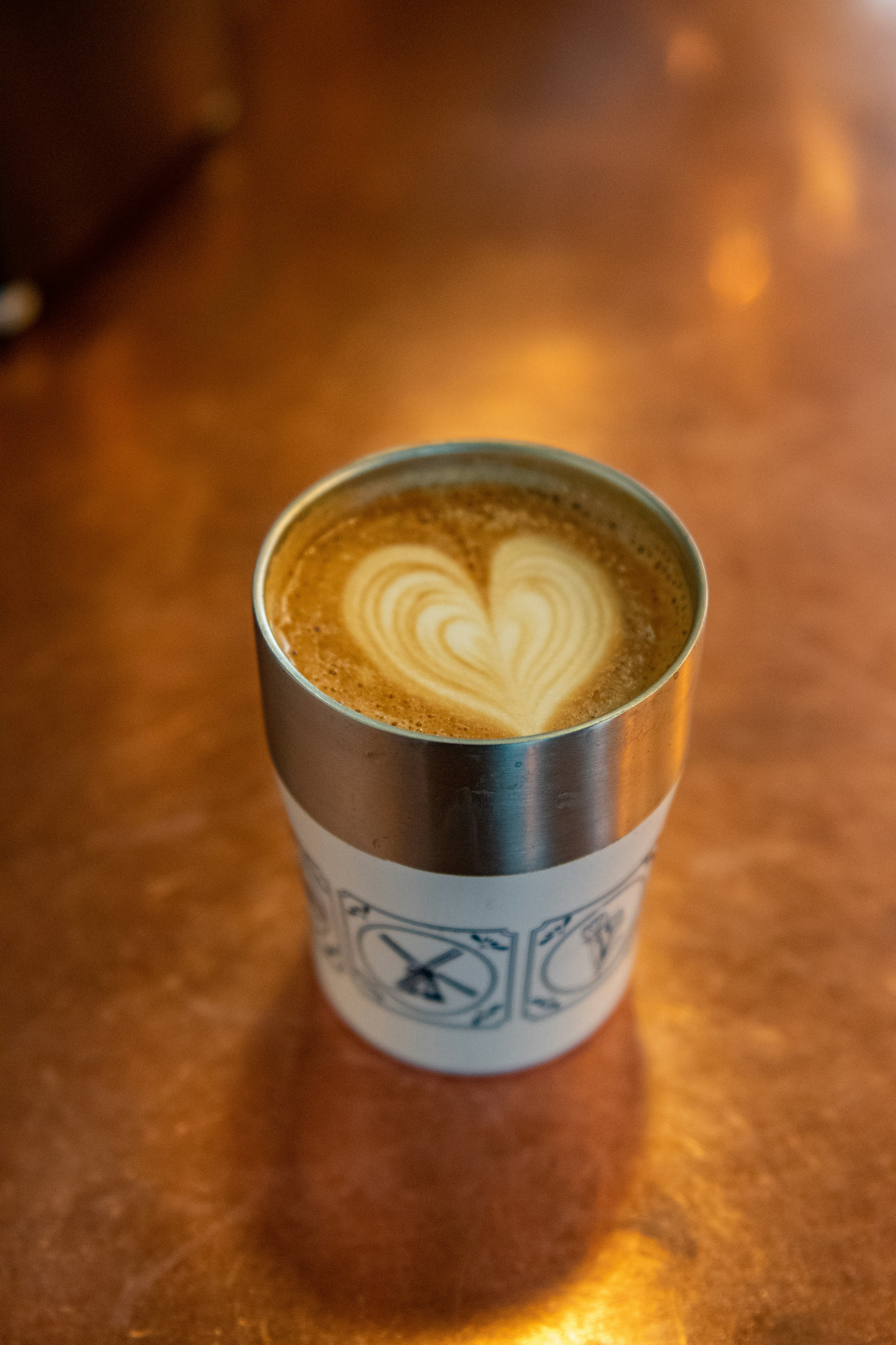 Latte with heart-shaped foam art in a white and metal cup on a copper table.