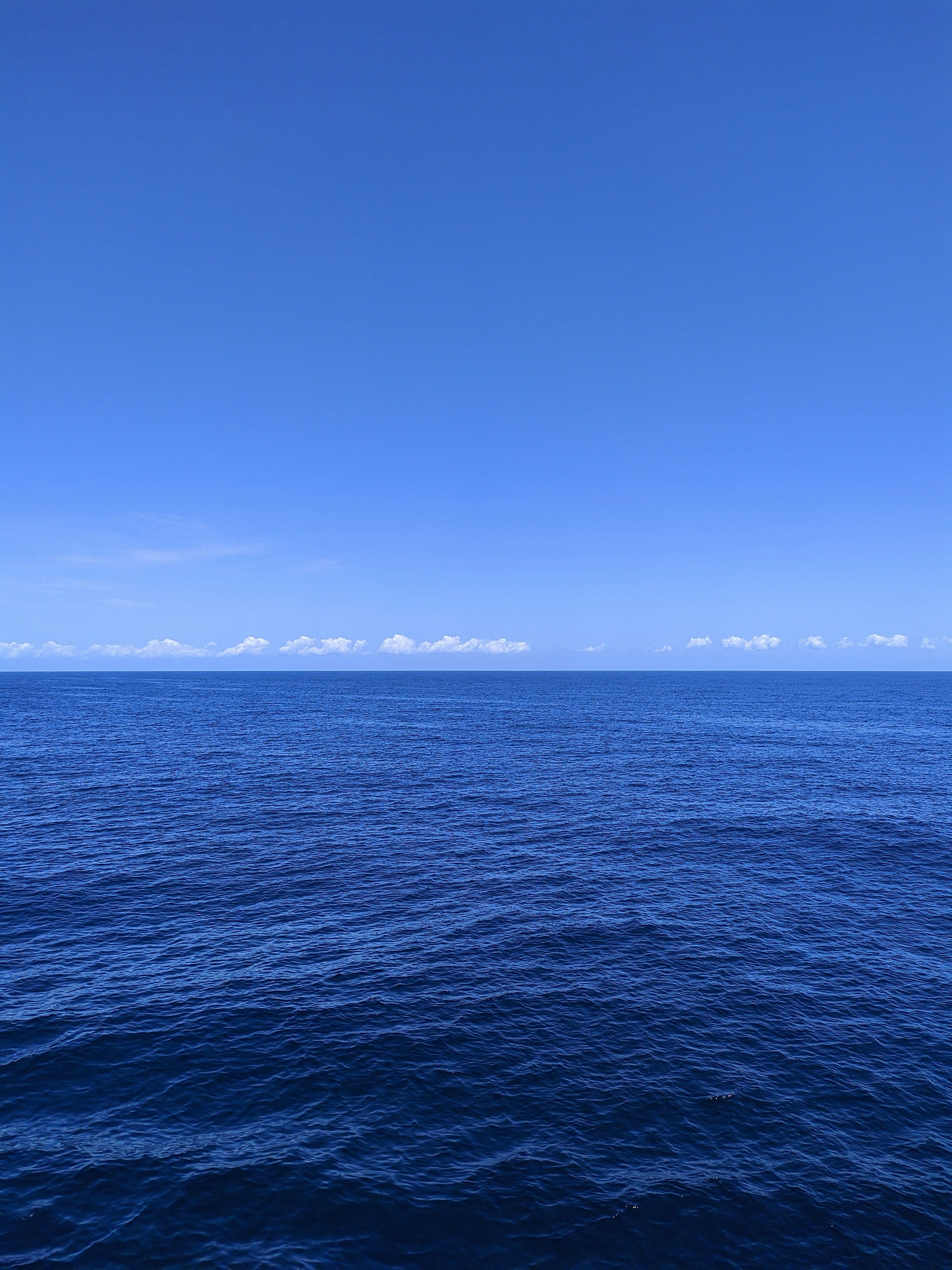Vast ocean meeting a clear blue sky with wispy clouds on the horizon.