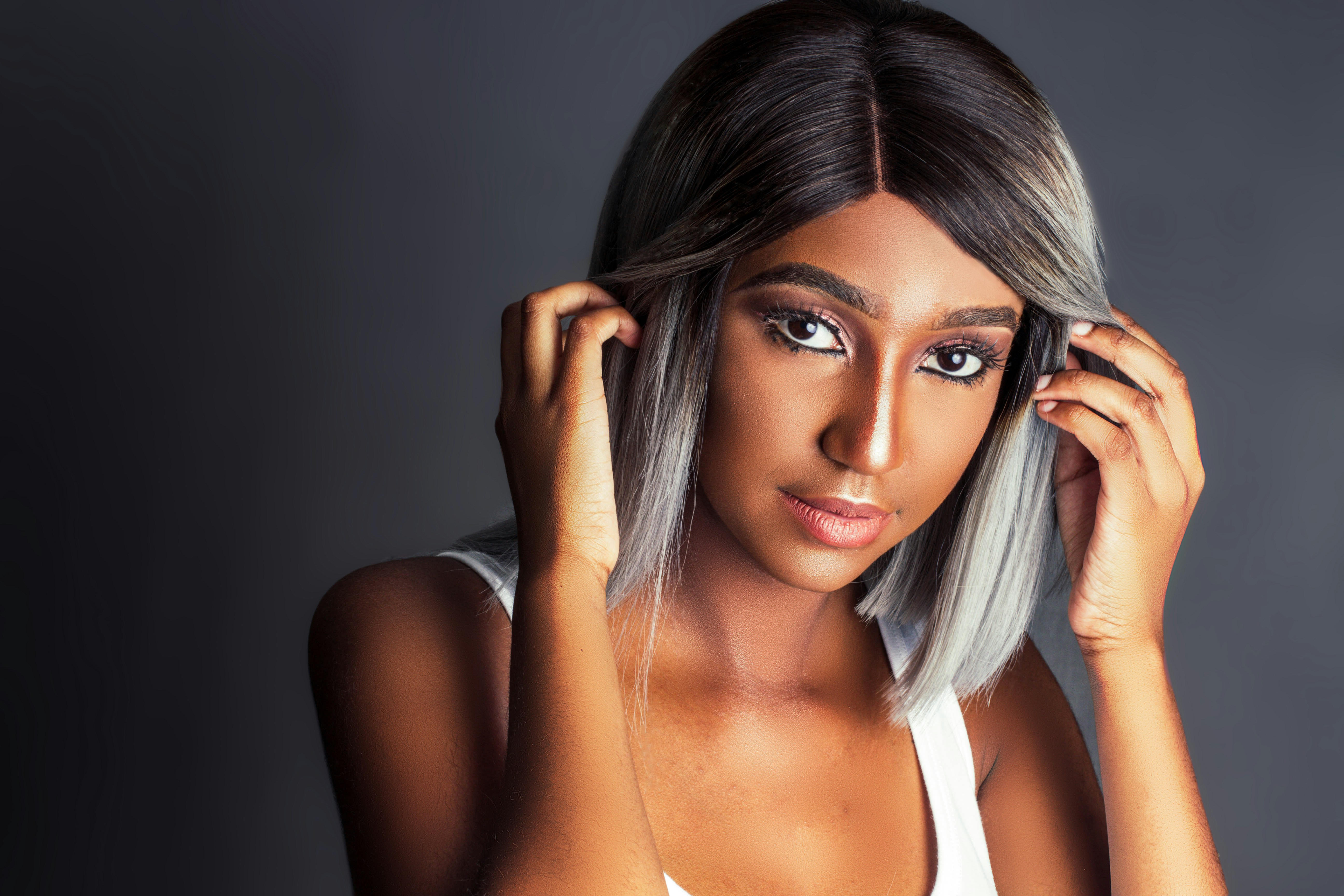 A woman with a stylish bob hairstyle gently touches her hair, exuding confidence against a soft gray backdrop.