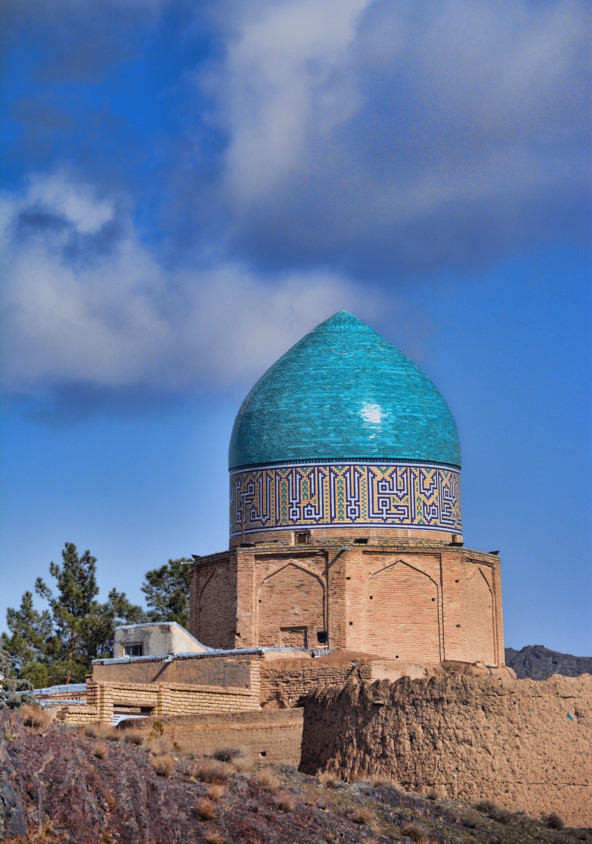 Historic mausoleum with a striking turquoise dome, set against a backdrop of blue skies and rugged terrain.