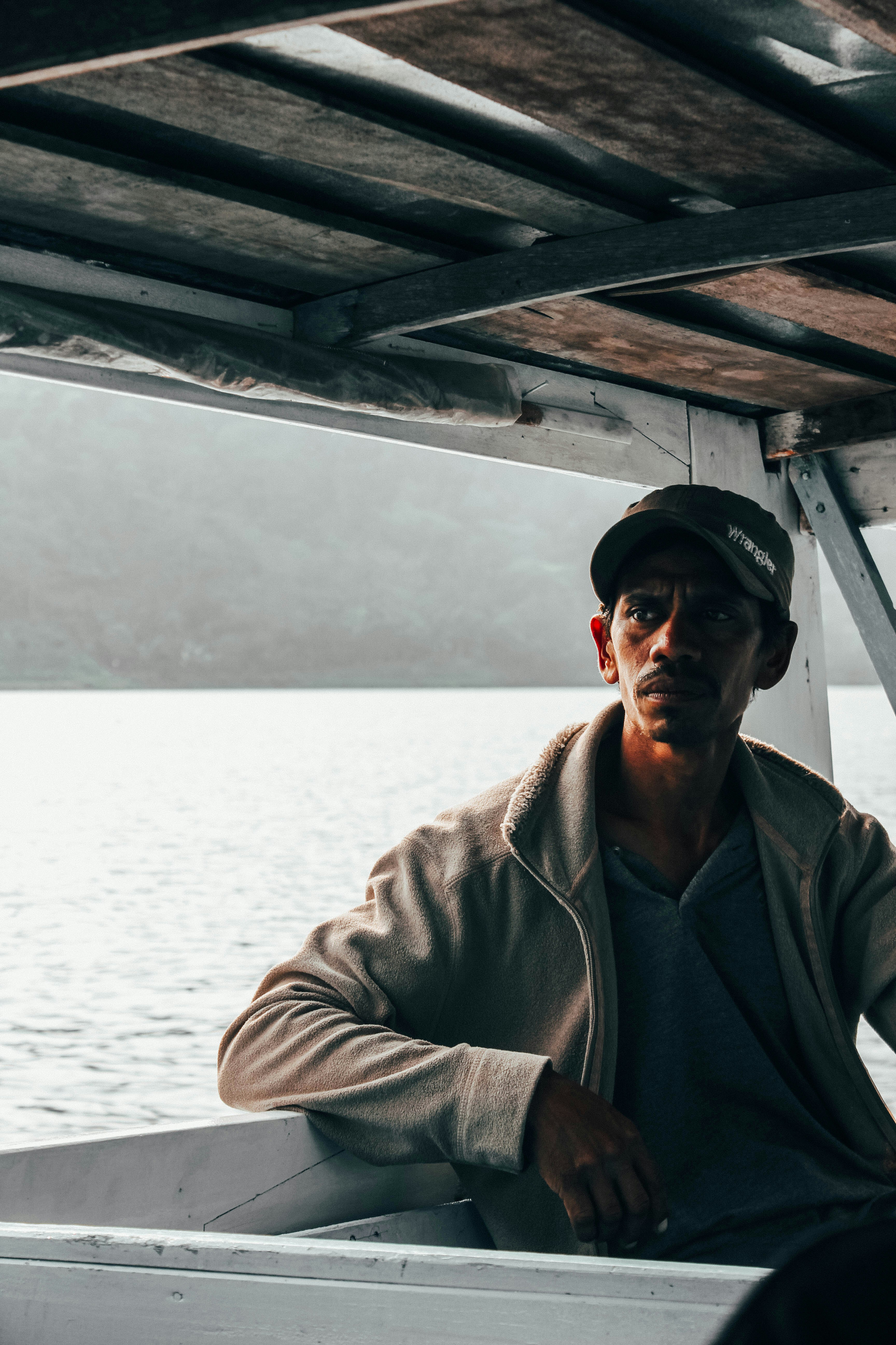 A contemplative man seated in a boat, gazing towards the water, with soft light illuminating his features. The serene lake and surrounding nature create a tranquil atmosphere.