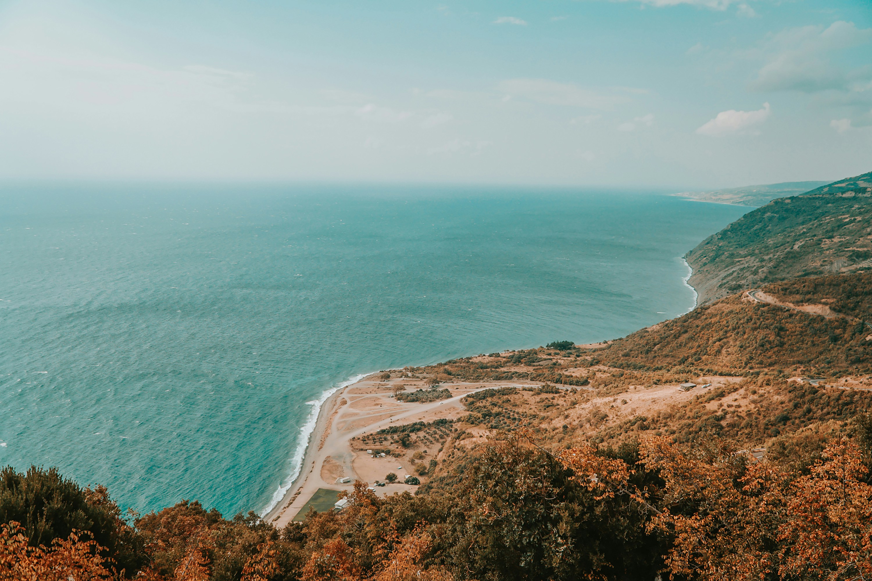 Expansive view of a tranquil coastline with rolling hills and a vast blue sea under a clear sky.