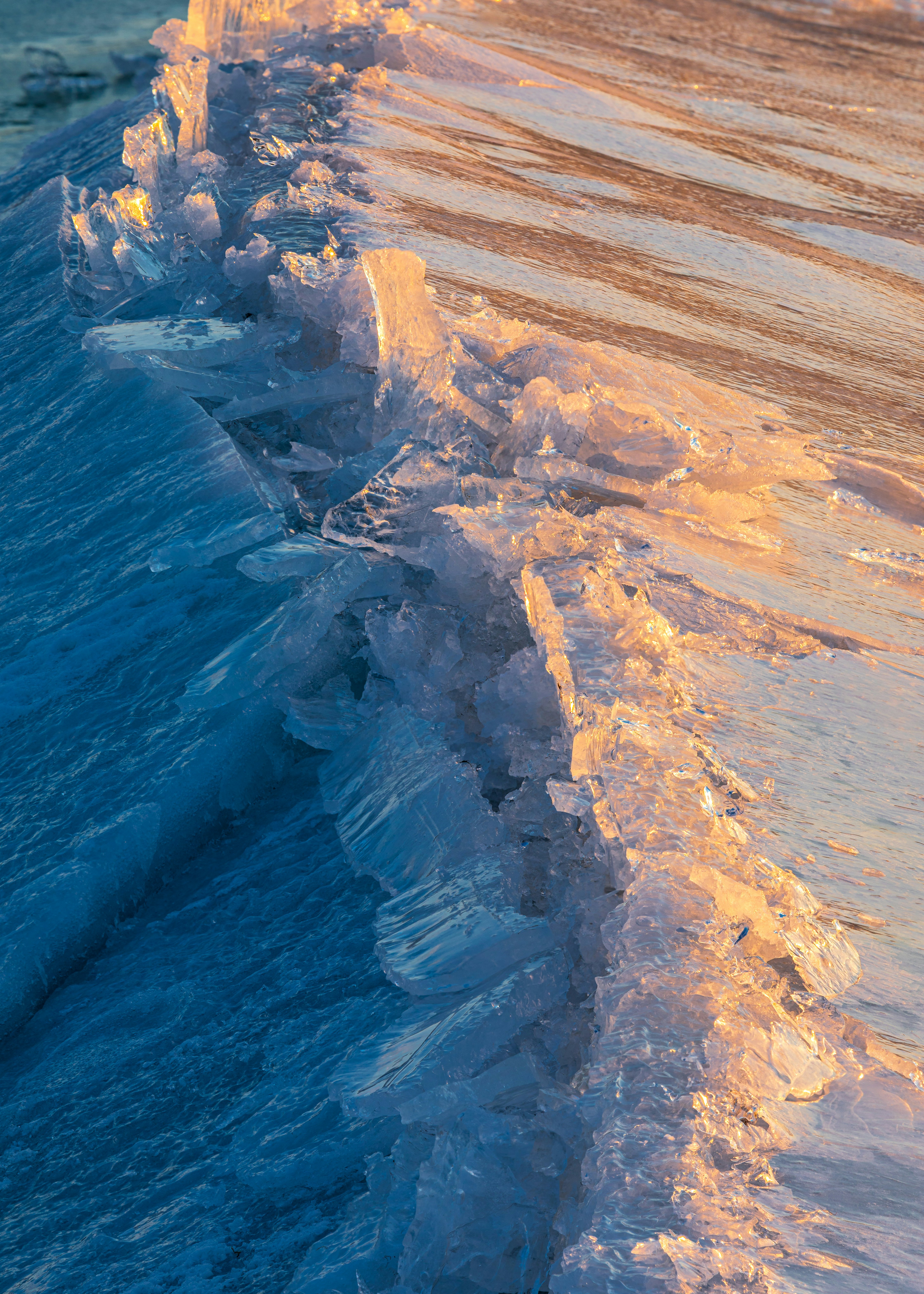 Jagged ice formations contrast against a shimmering, reflective surface, capturing the interplay of light and texture in a winter landscape.