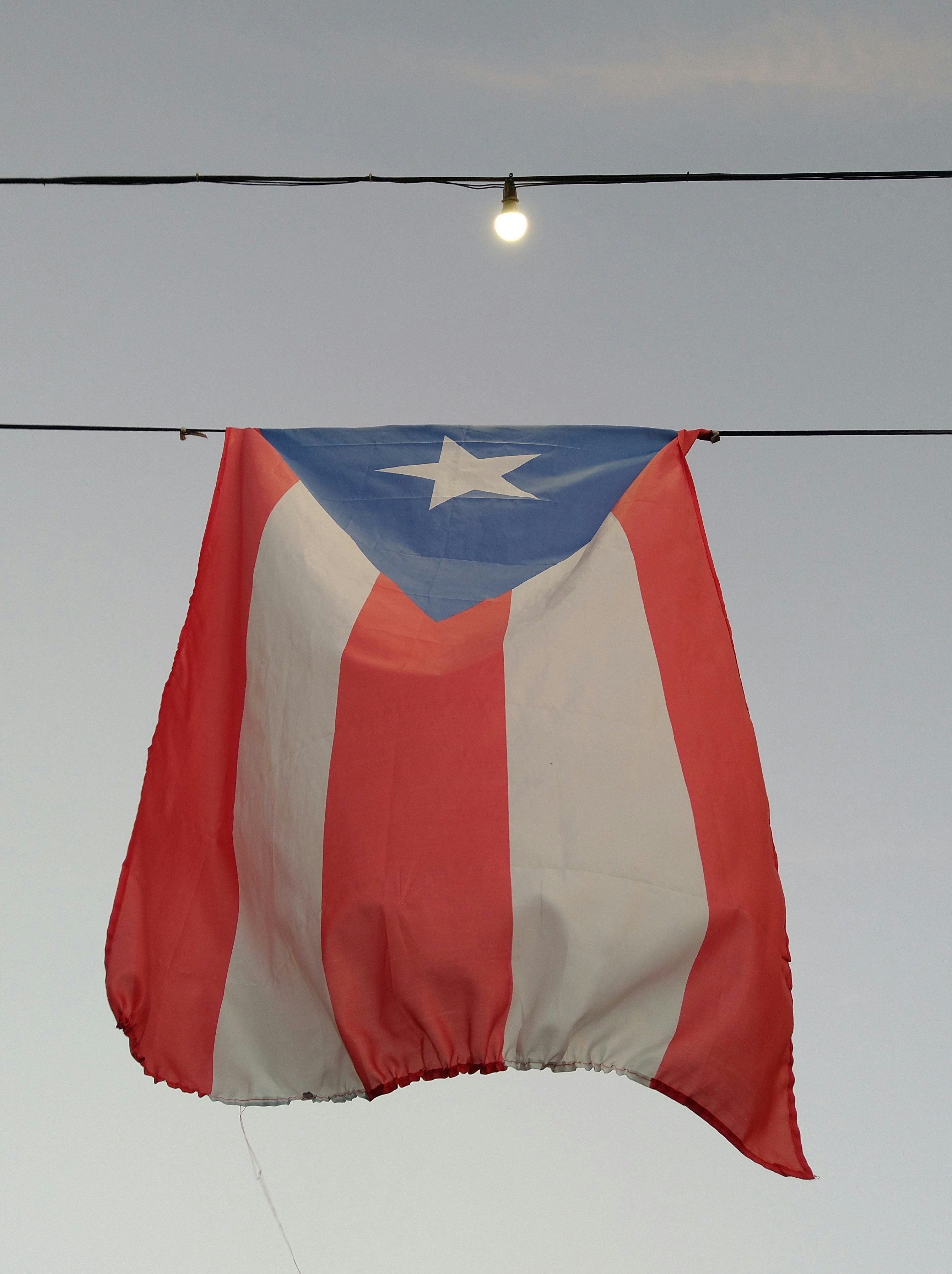 Puerto Rican flag displayed against a soft twilight sky, accentuated by a hanging light bulb above. 