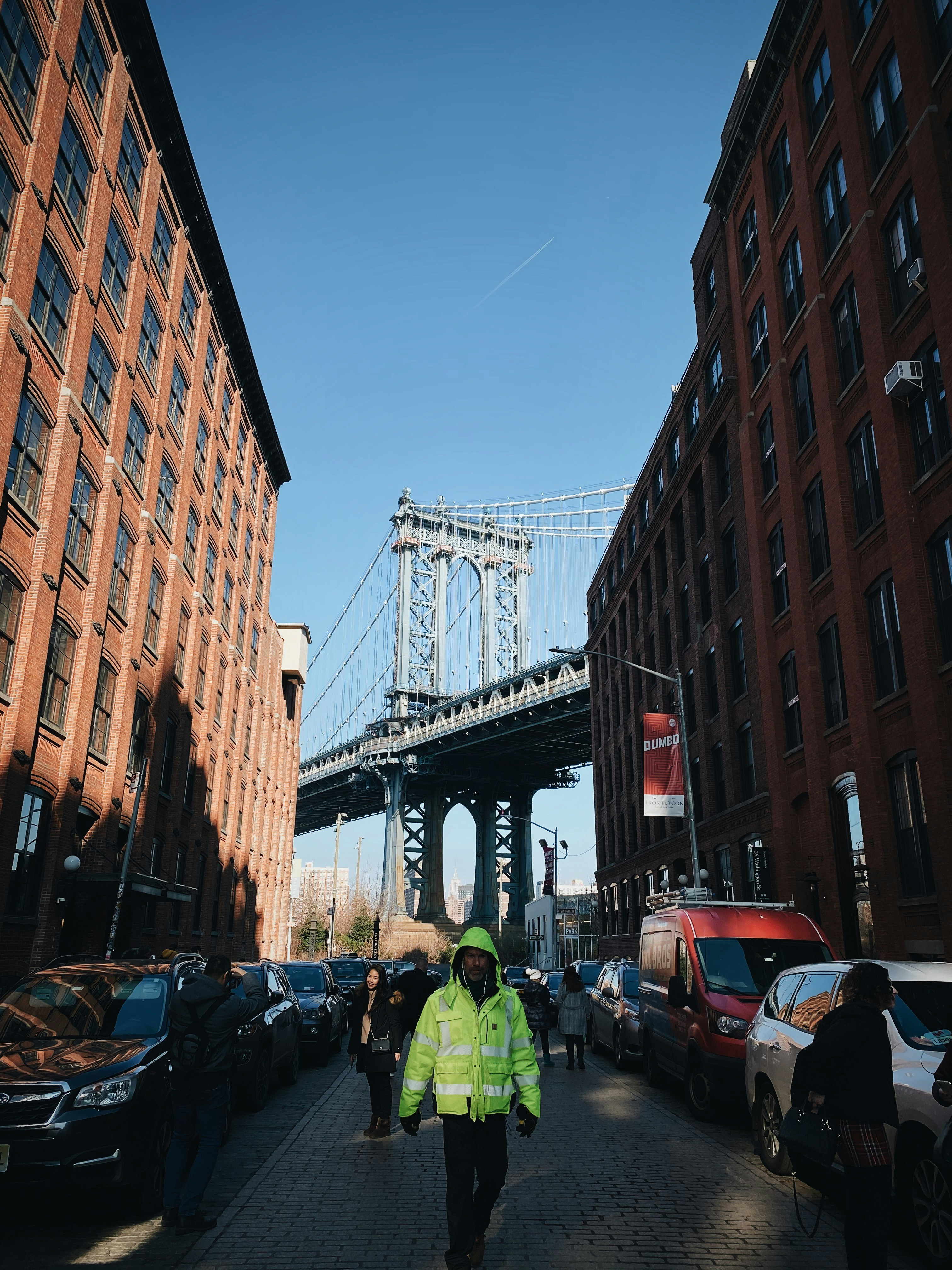 Neon Vest in a Brick Canyon: A pedestrian strides toward the Manhattan Bridge