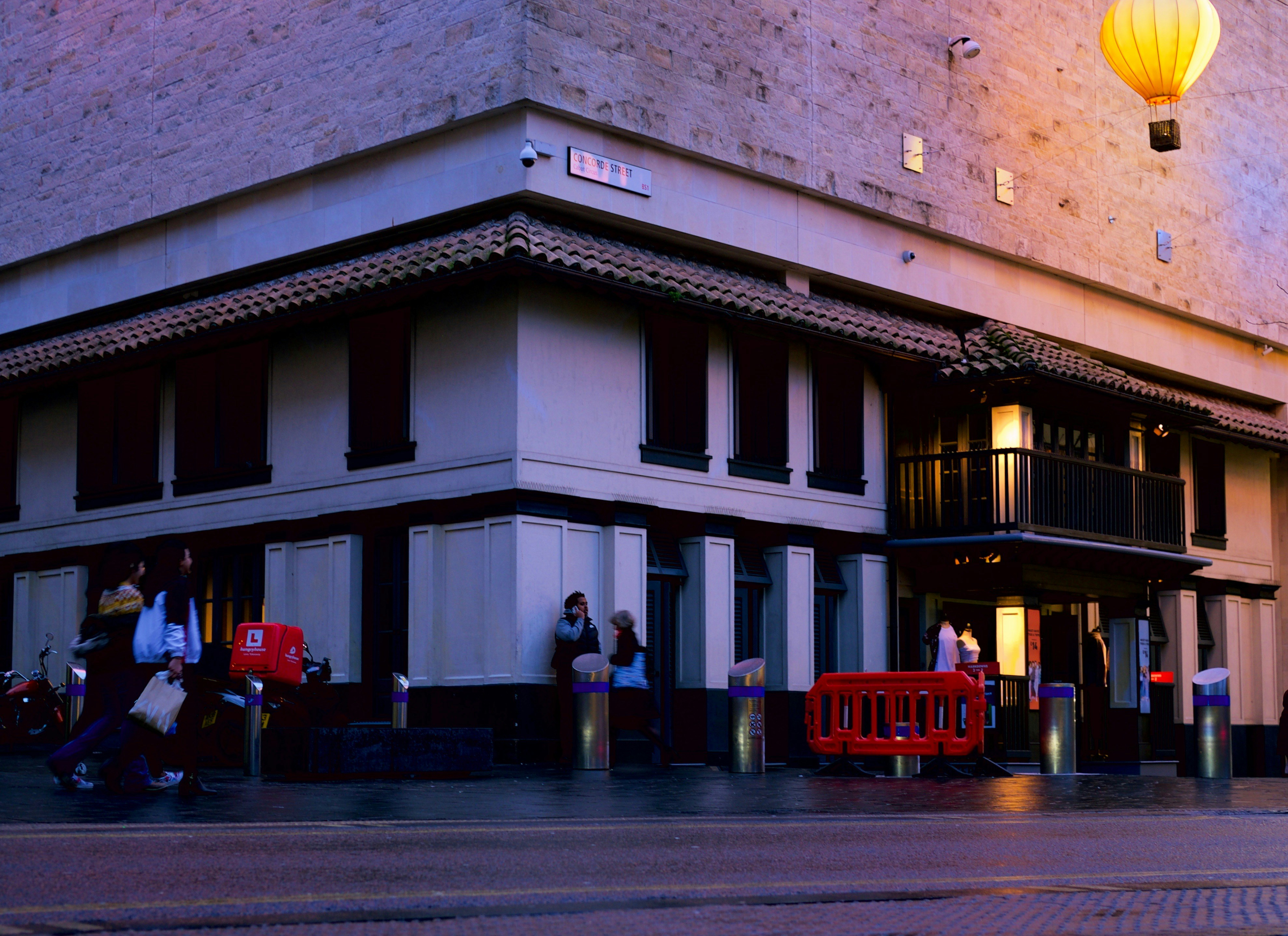 People gather near a dimly lit building corner under a glowing streetlight at dusk.