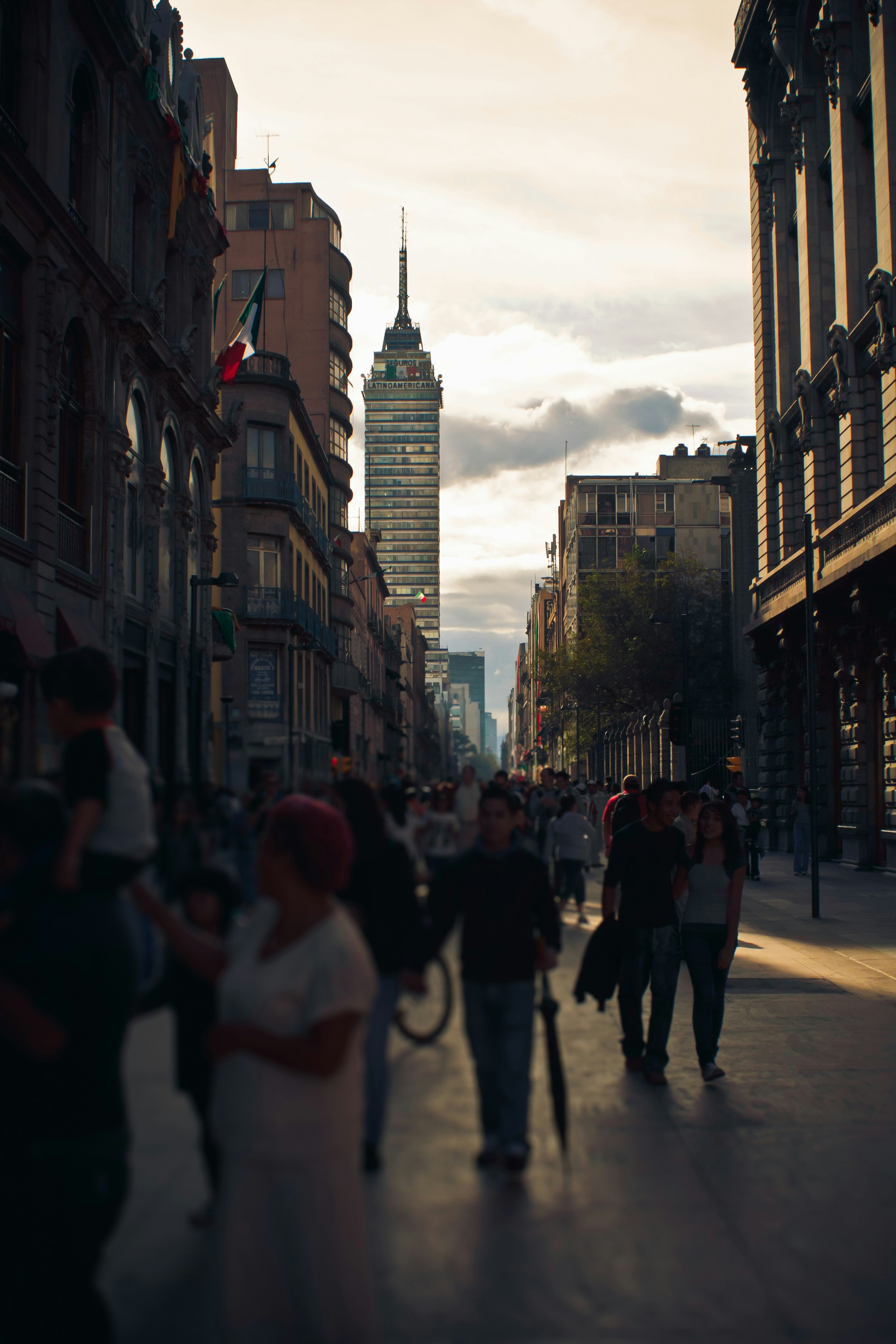 Bustling street scene in Mexico City with pedestrians and historical architecture, featuring the iconic Torre Latinoamericana in the background. 