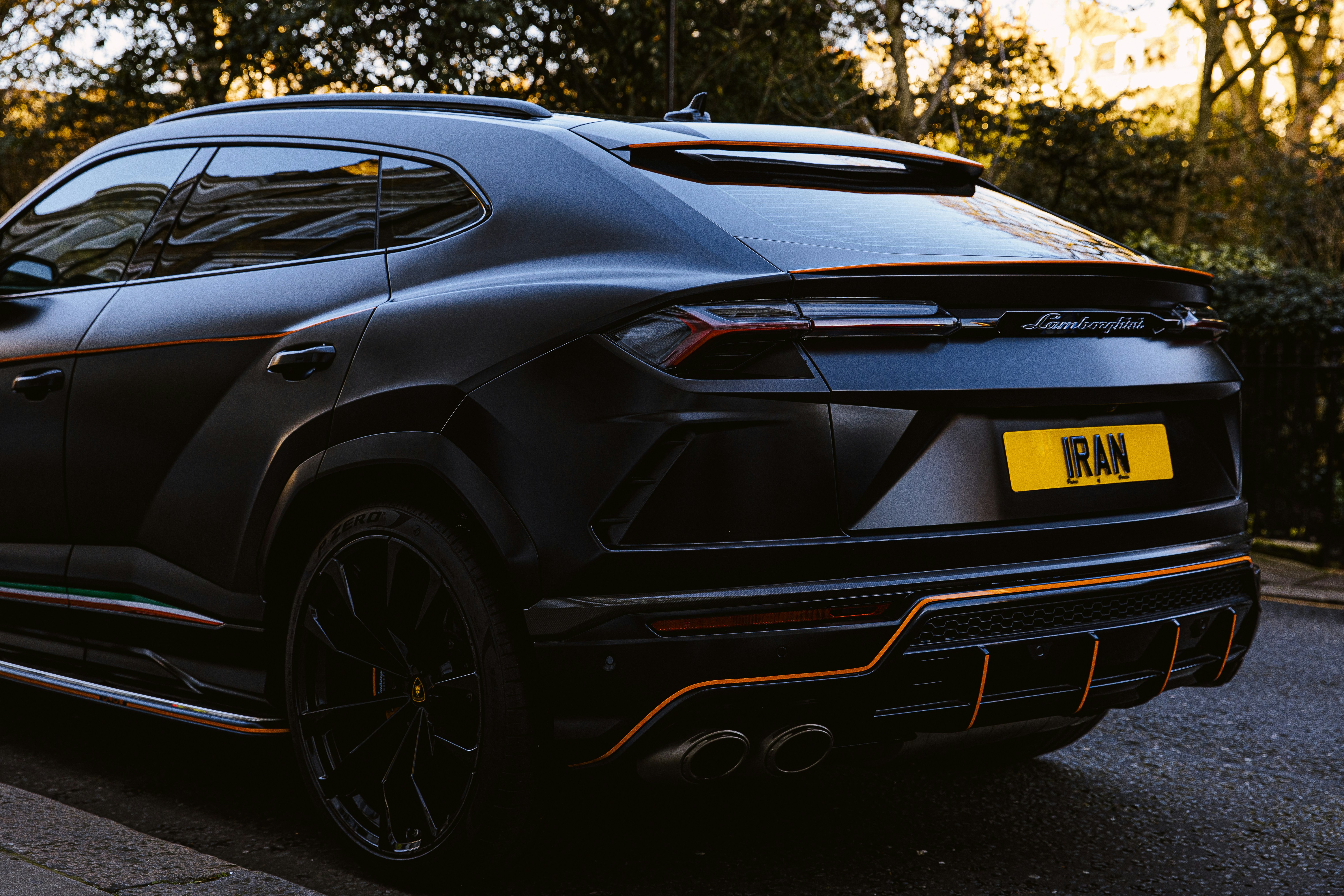 Sleek black Lamborghini Urus parked on a city street with trees in the background.