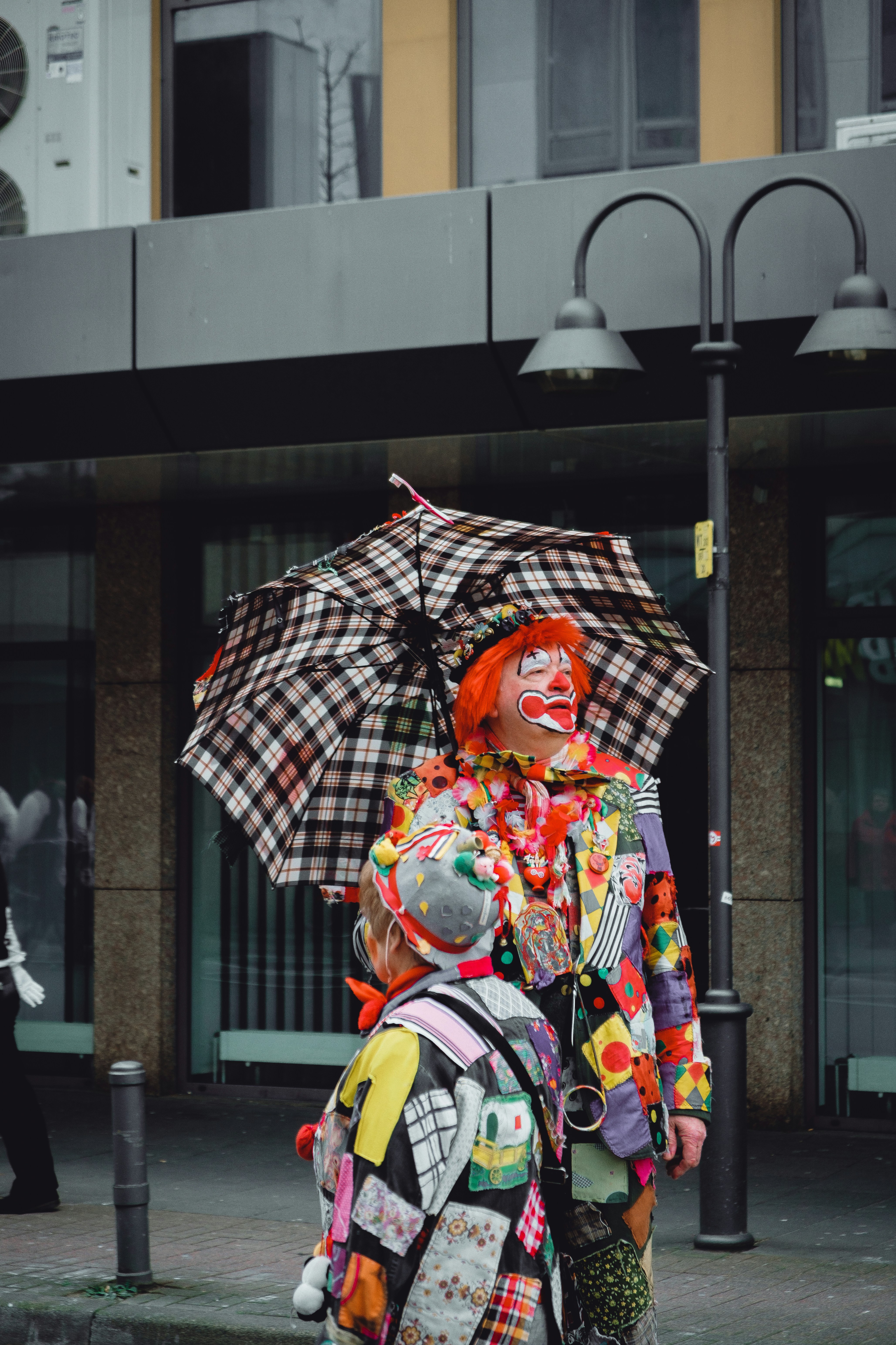 Patchwork Clown Under a Plaid Umbrella in a City Street