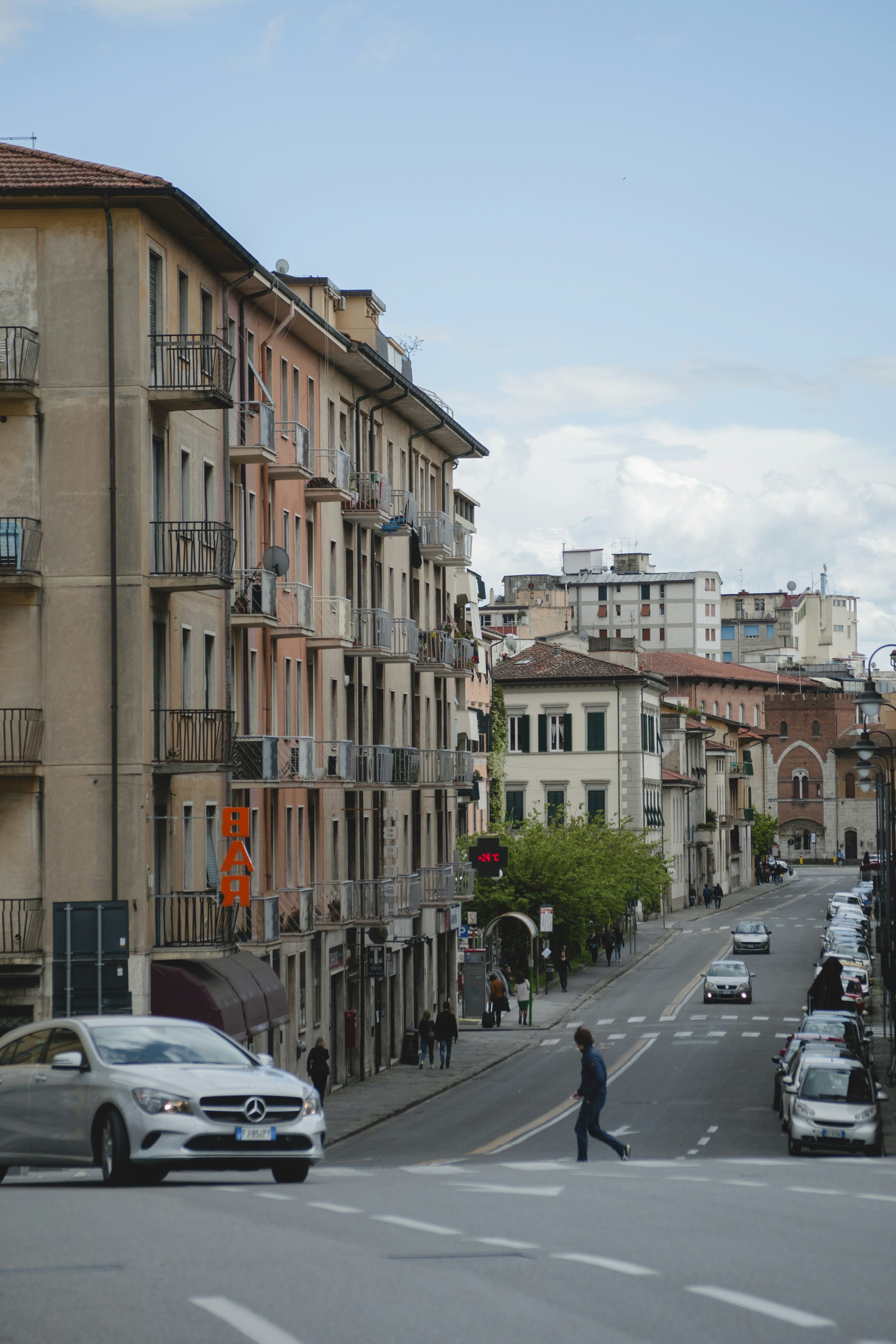 A bustling city street scene featuring colorful buildings, pedestrians, and cars navigating the road. The atmosphere reflects daily urban life.