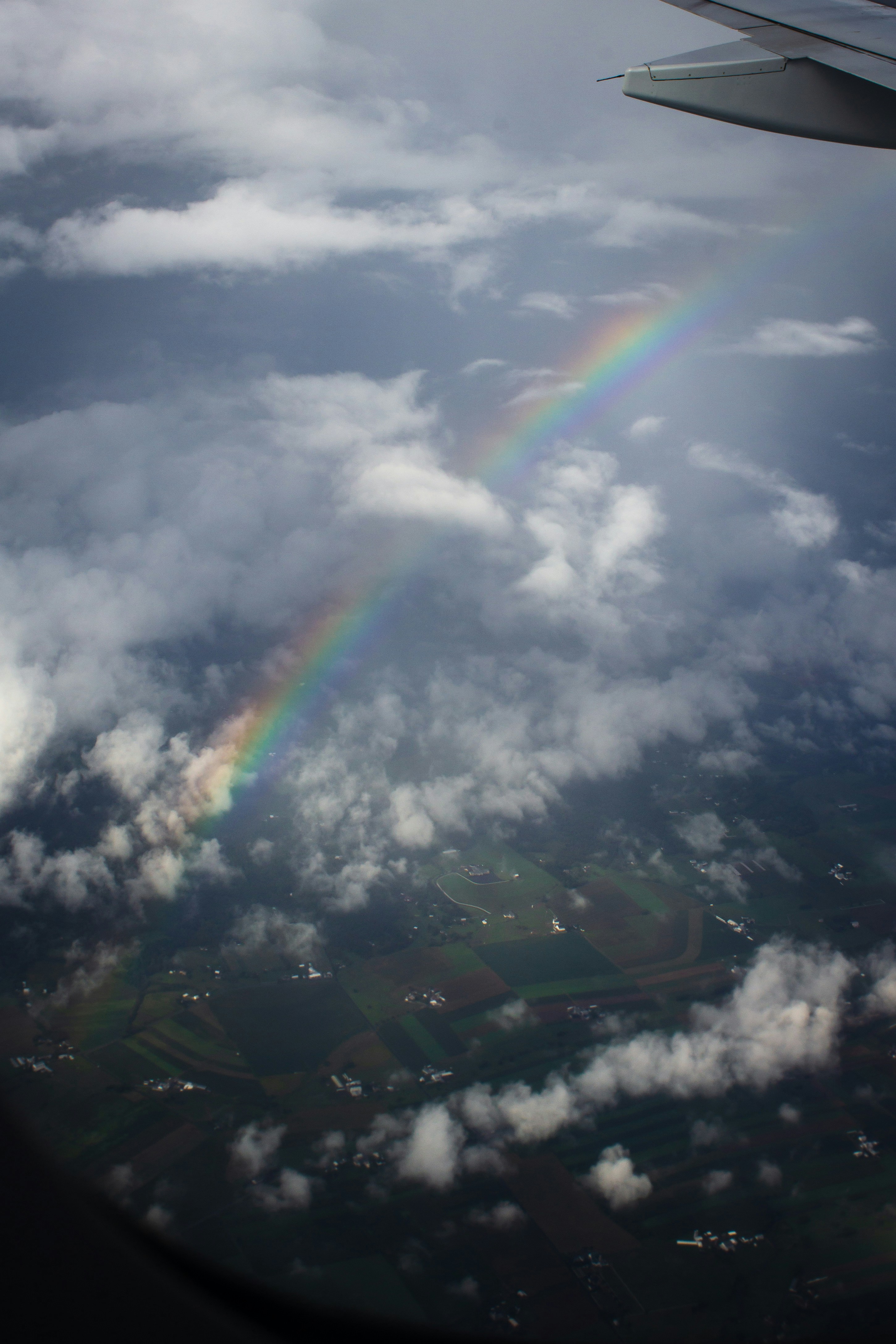 Rainbow Above the Clouds: A Flight-Window Moment over Patchwork Fields