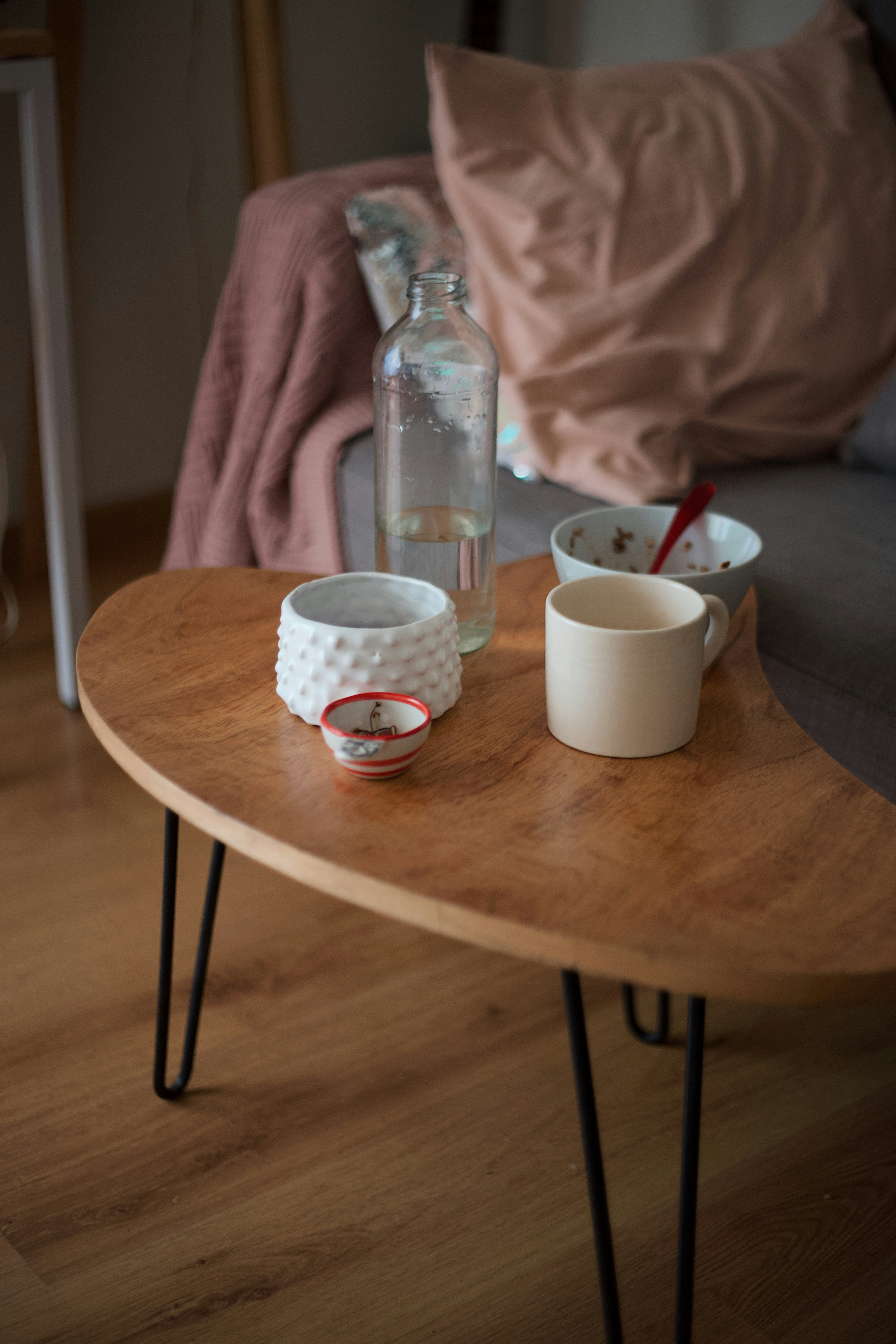 A wooden coffee table adorned with a variety of cups, a water bottle, and a cozy blanket draped over a nearby sofa. The scene evokes a warm, inviting atmosphere.