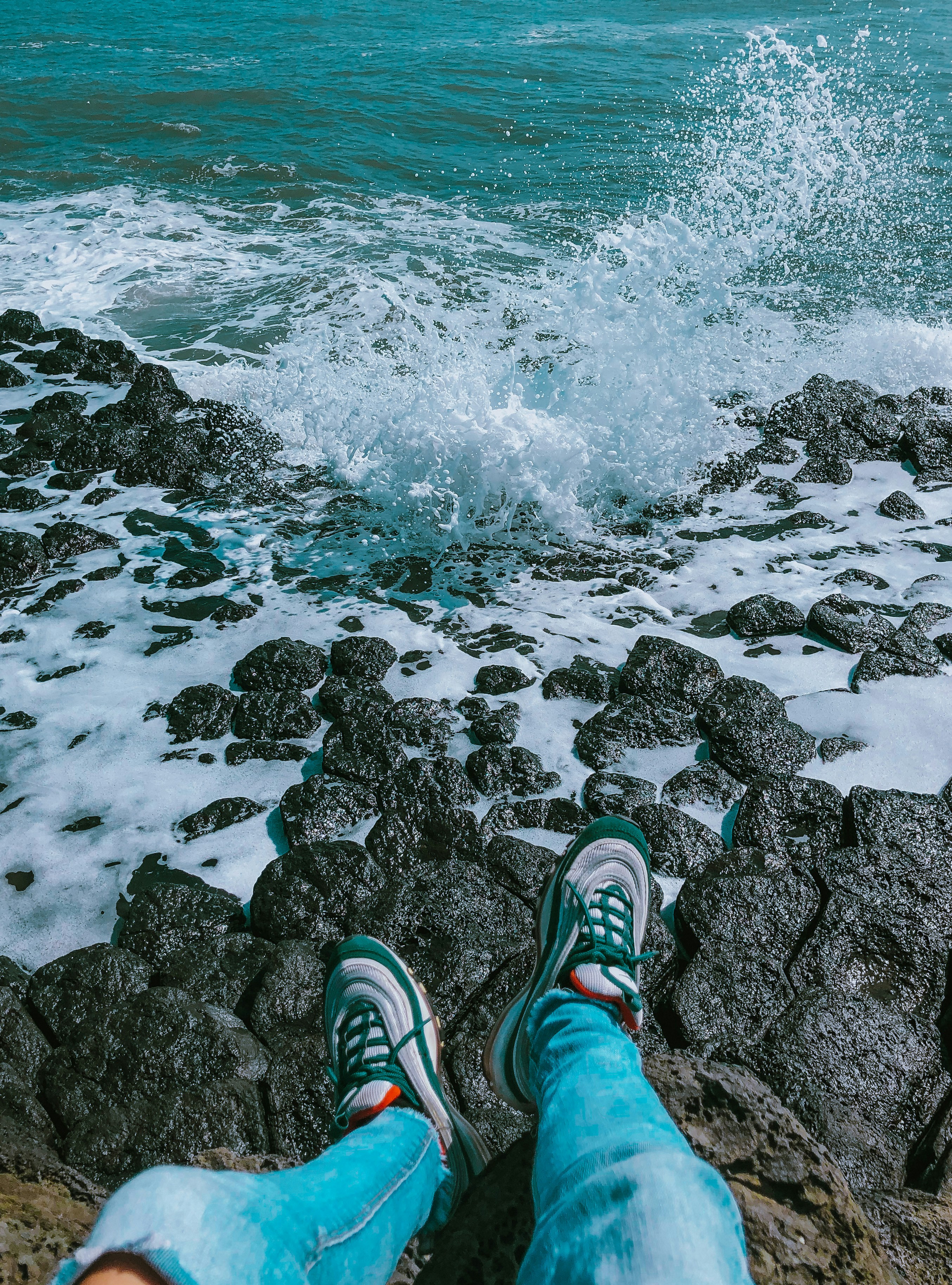 Feet resting on rocky shoreline as ocean waves crash nearby, creating a dynamic interaction between land and sea.