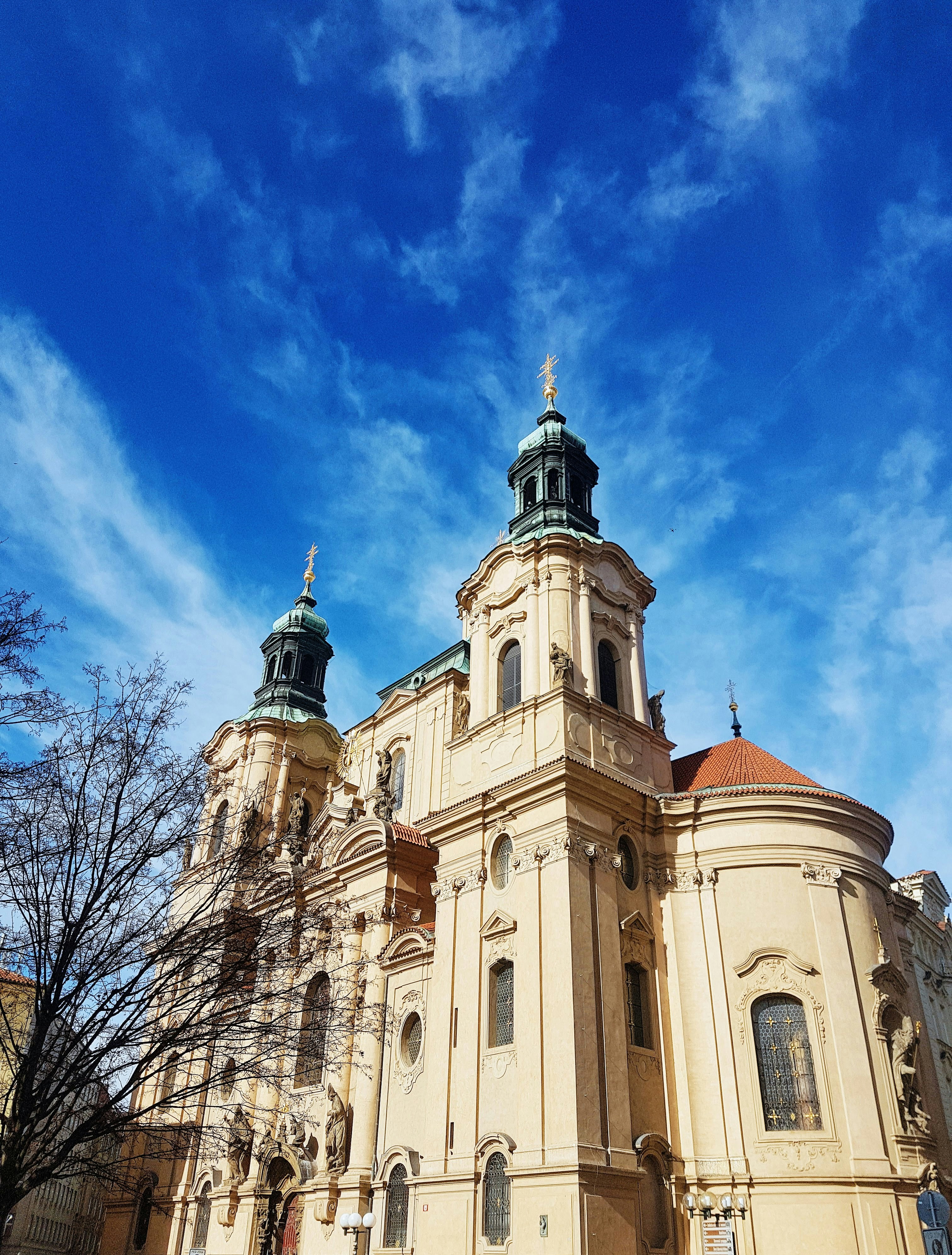 Baroque church facade adorned with intricate details and domes, set against a vibrant blue sky. The scene captures a blend of history and artistry.