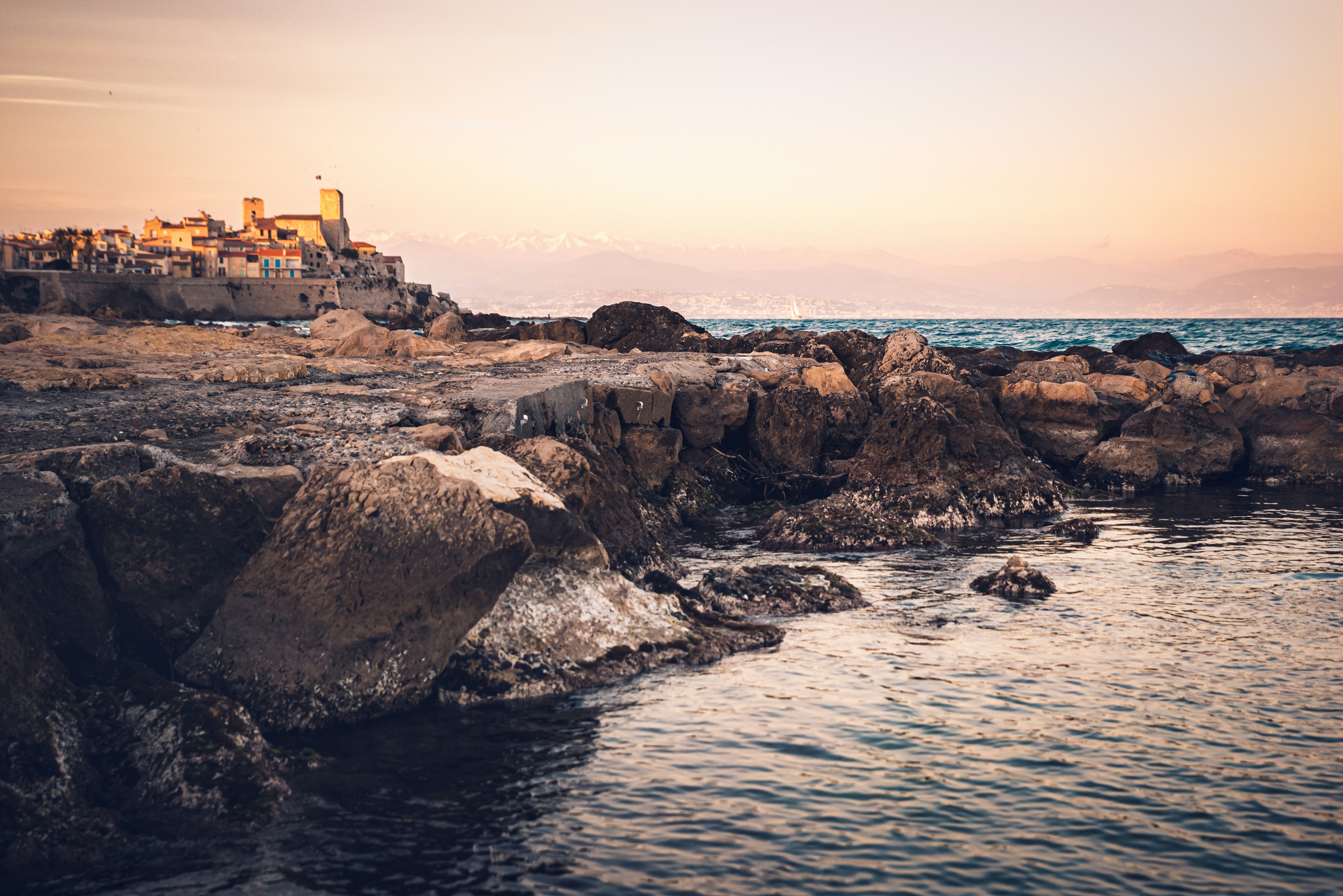 Rocky coastline of Antibes with the sea under a pastel sunset sky.