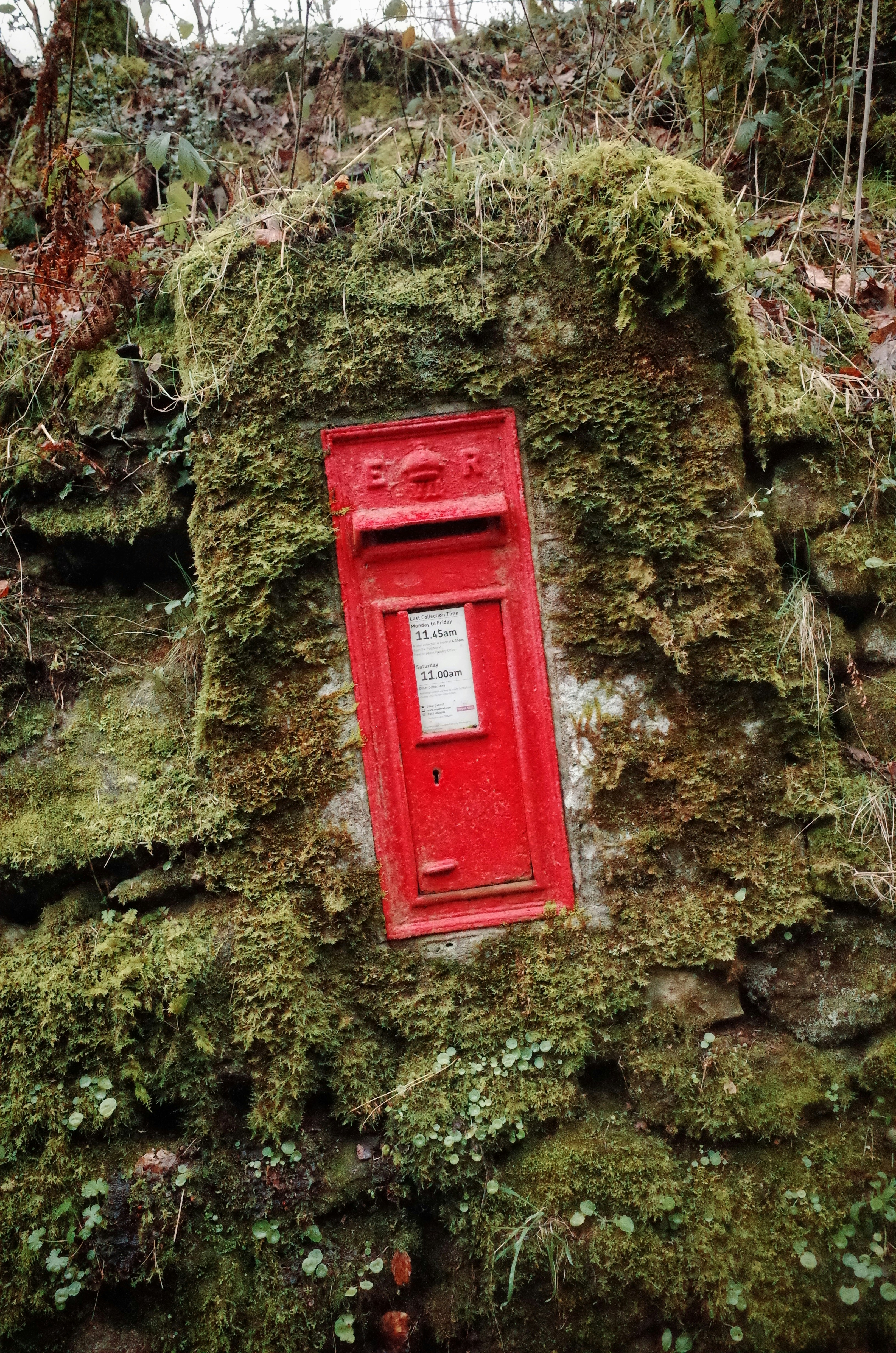 Weathered red postbox embedded in a moss-covered stone wall, showcasing the passage of time and nature's reclamation.