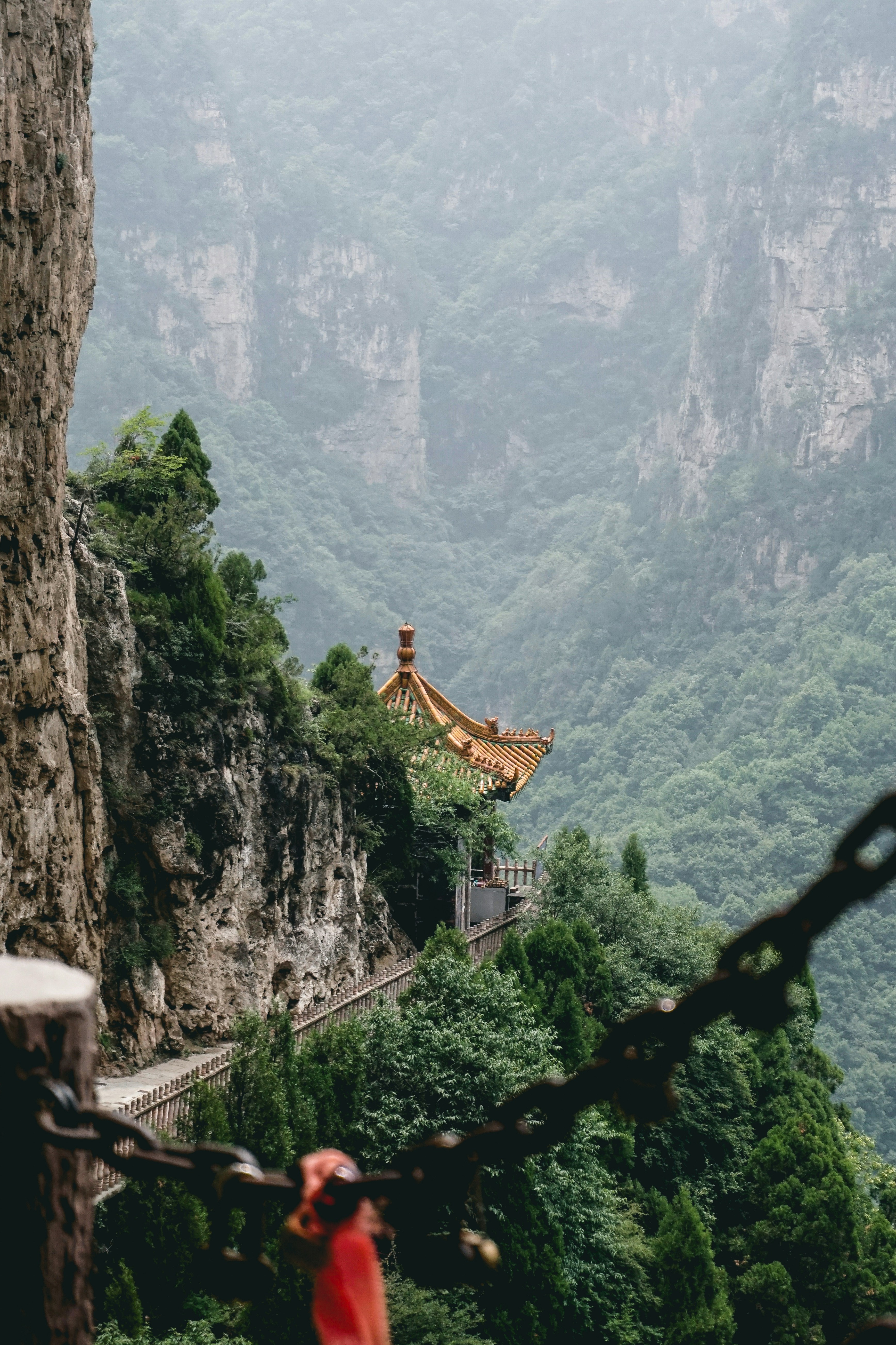 Traditional pagoda perched on a cliffside, surrounded by lush green mountains shrouded in mist.