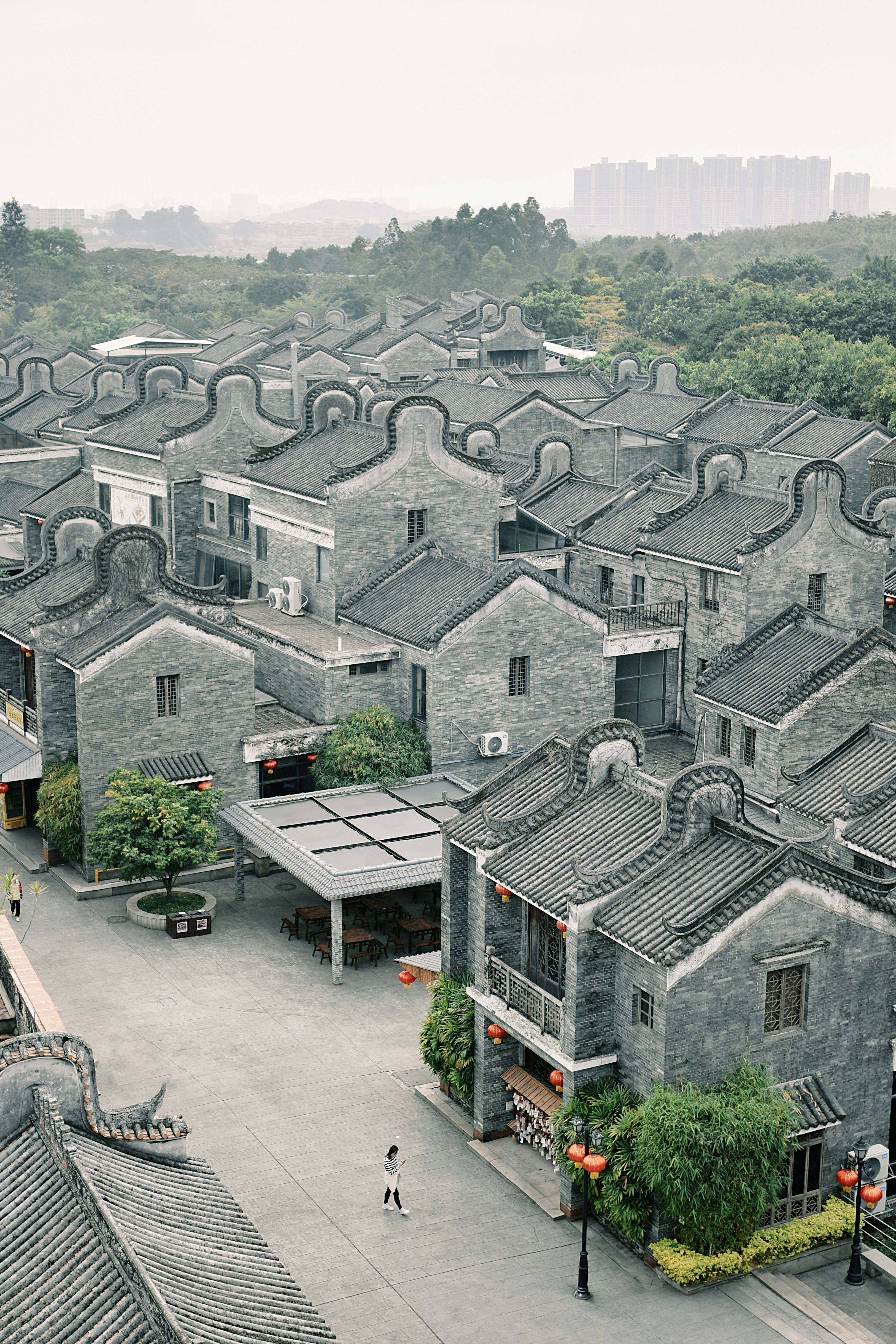 Aerial view of traditional gray stone buildings with curved roofs, showcasing a blend of historic and contemporary elements. A solitary figure walks through the courtyard.