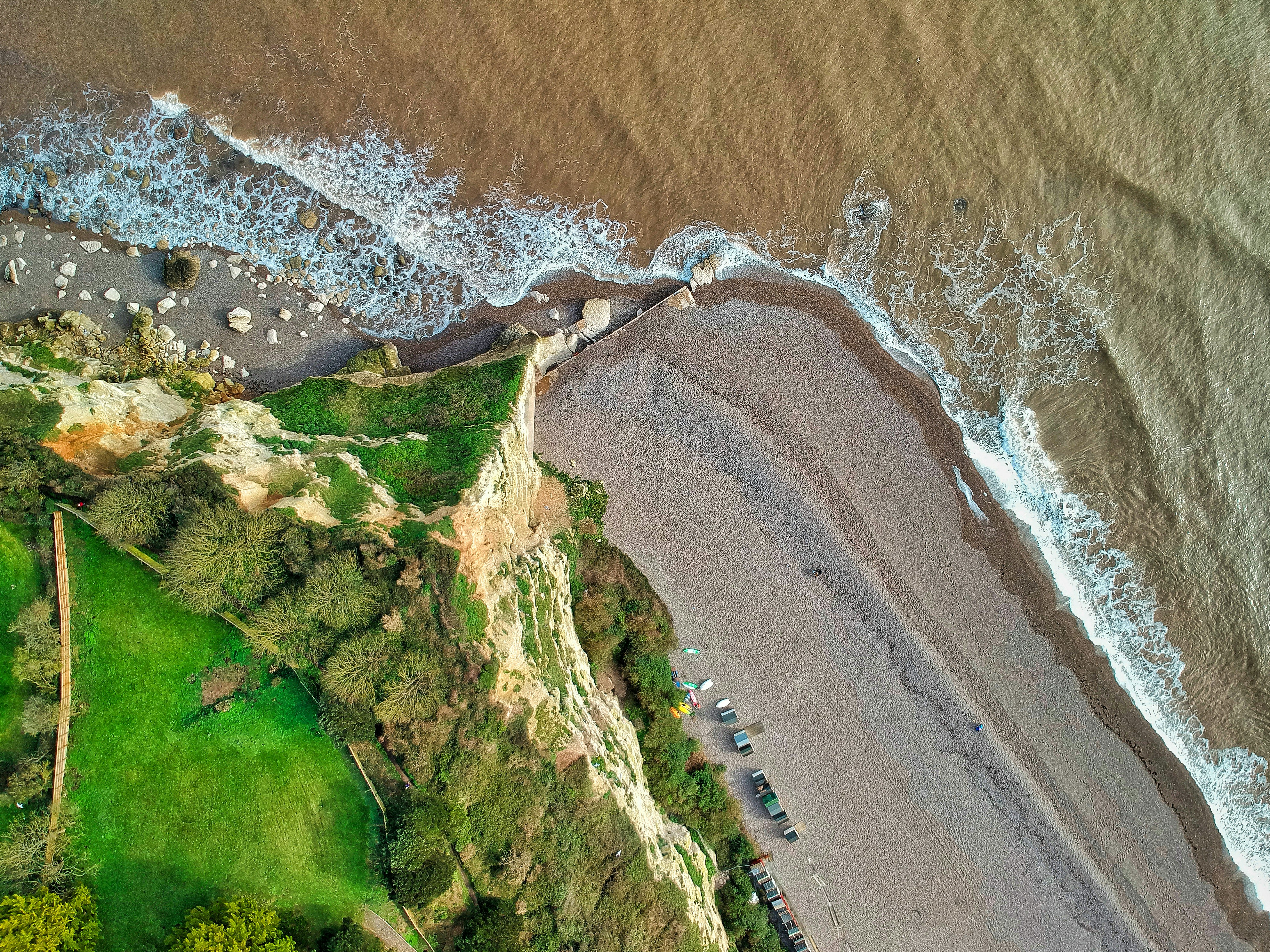 Aerial view of a rugged coastline where lush greenery meets a sandy beach, with waves gently lapping at the shore.