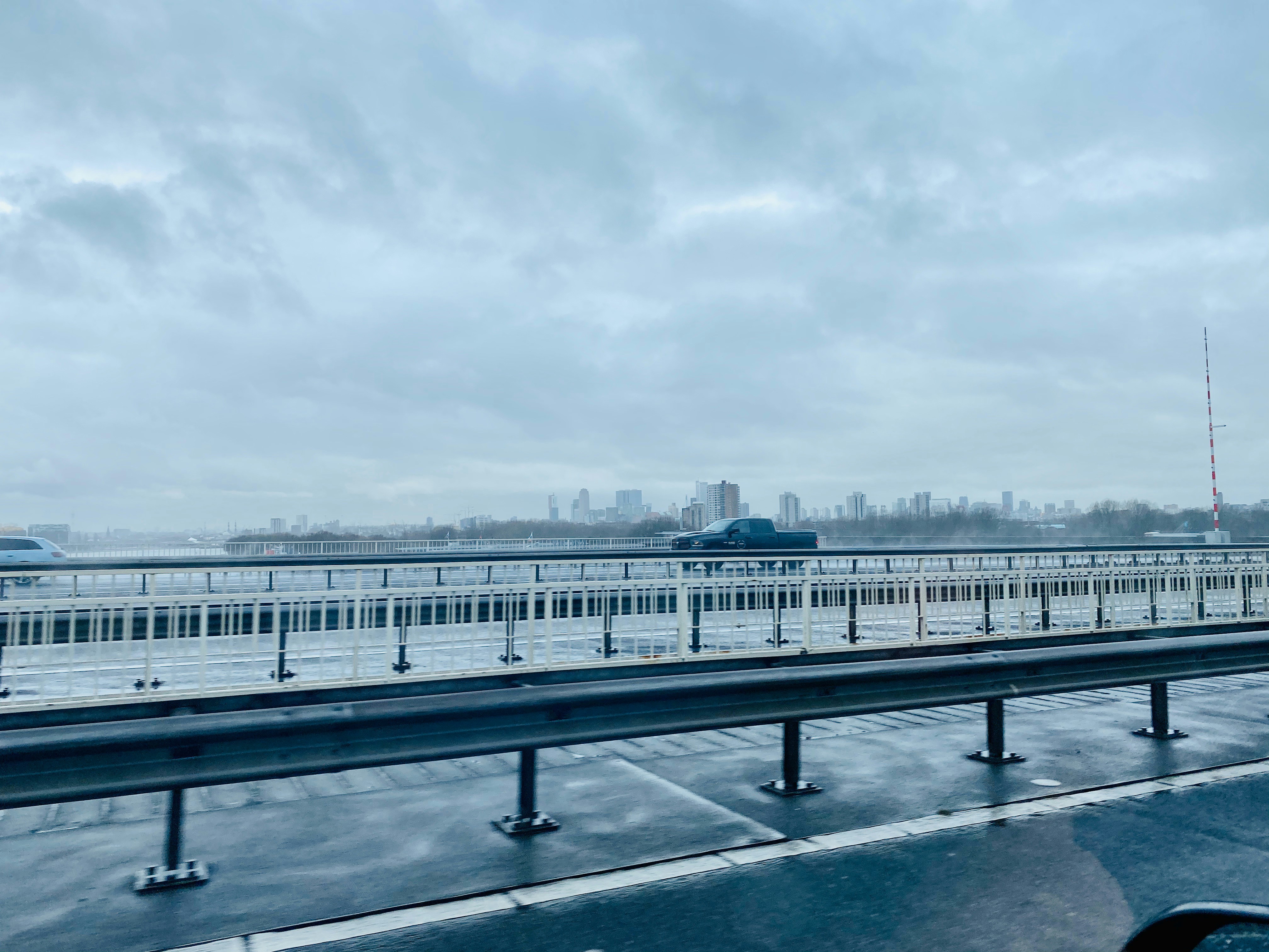 Blue sedan on a misty river bridge with distant city skyline