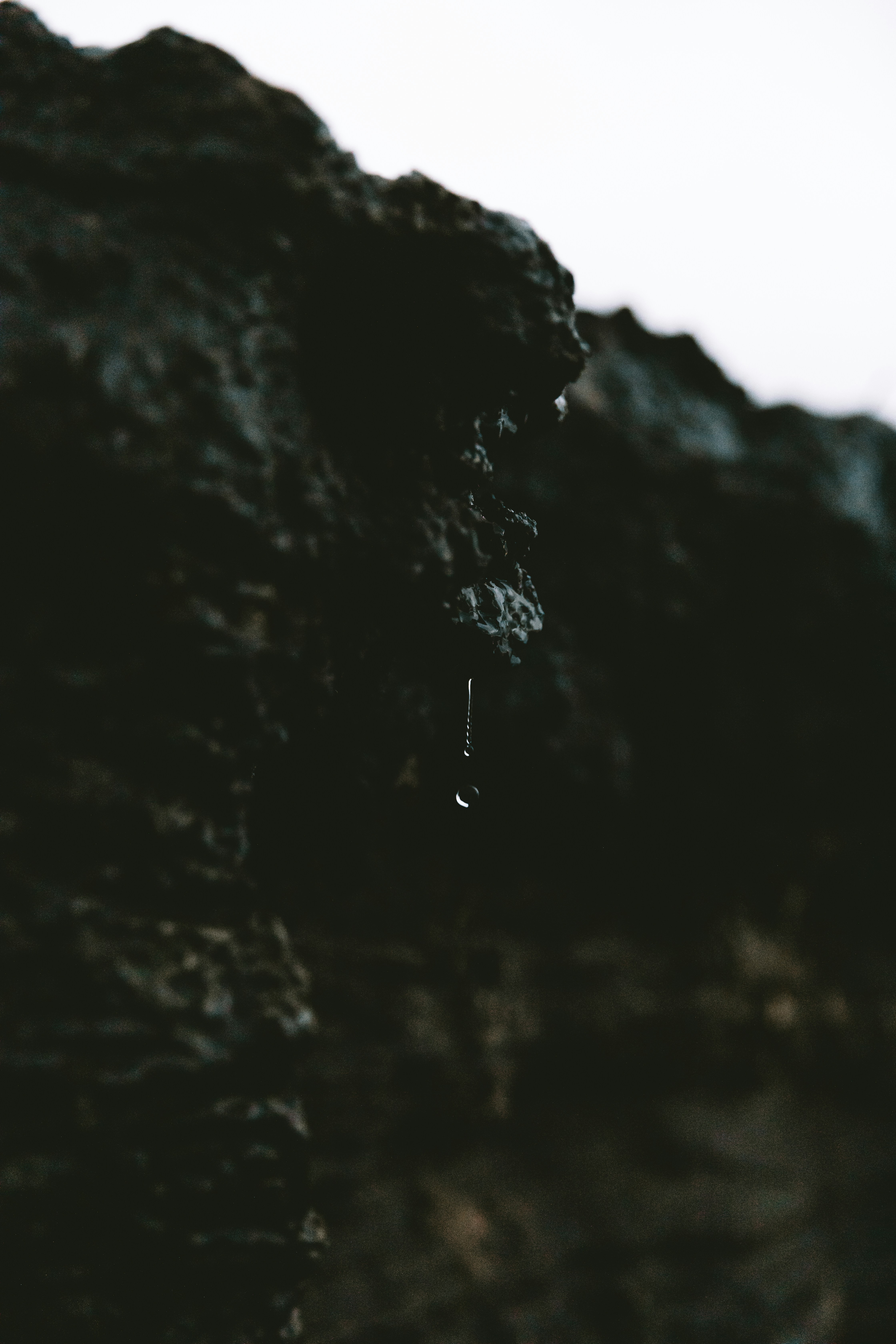 A solitary drop clings to a jagged cliff edge at dusk
