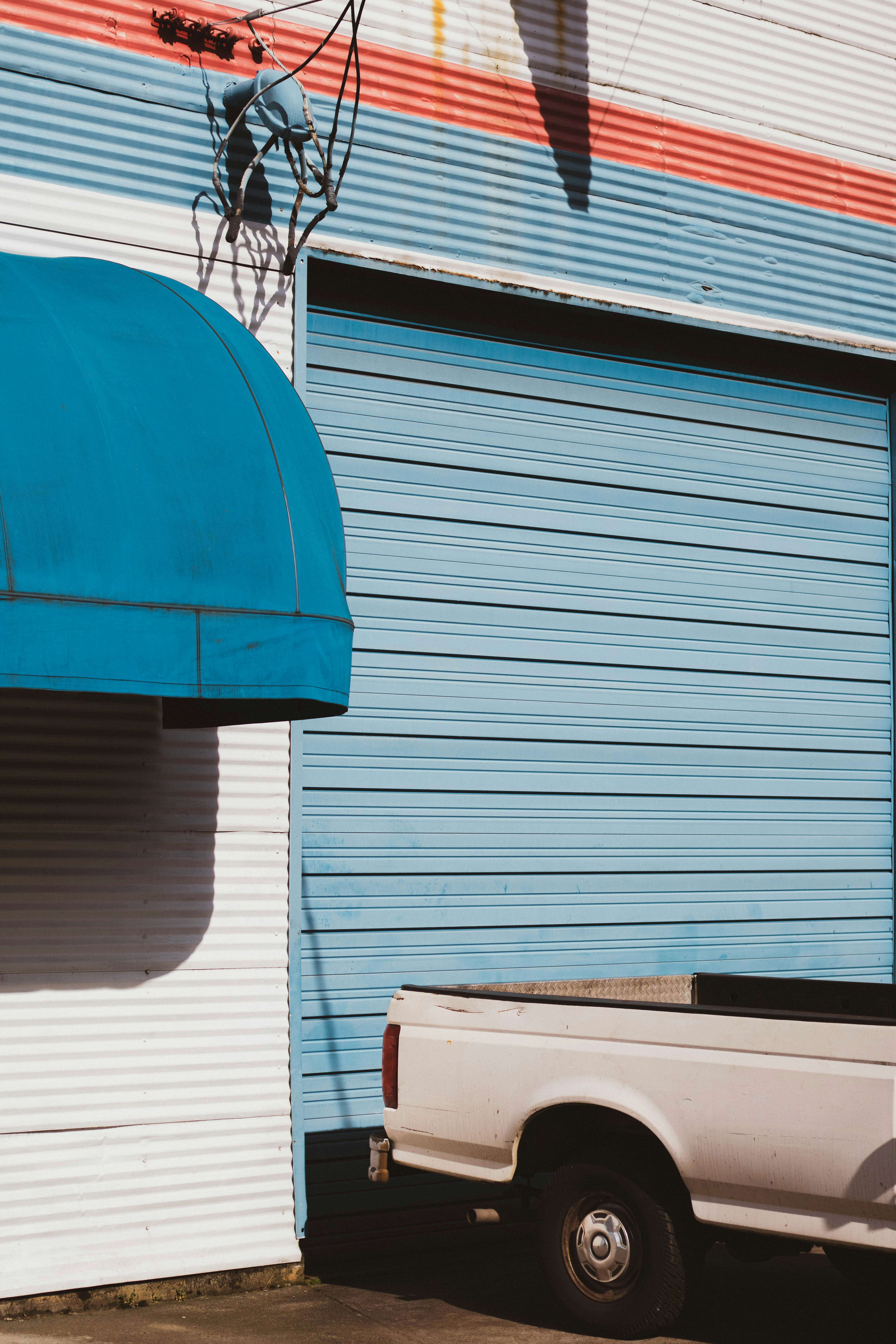 A white pickup truck parked beside a blue wall with a contrasting blue awning, highlighting urban textures and colors.