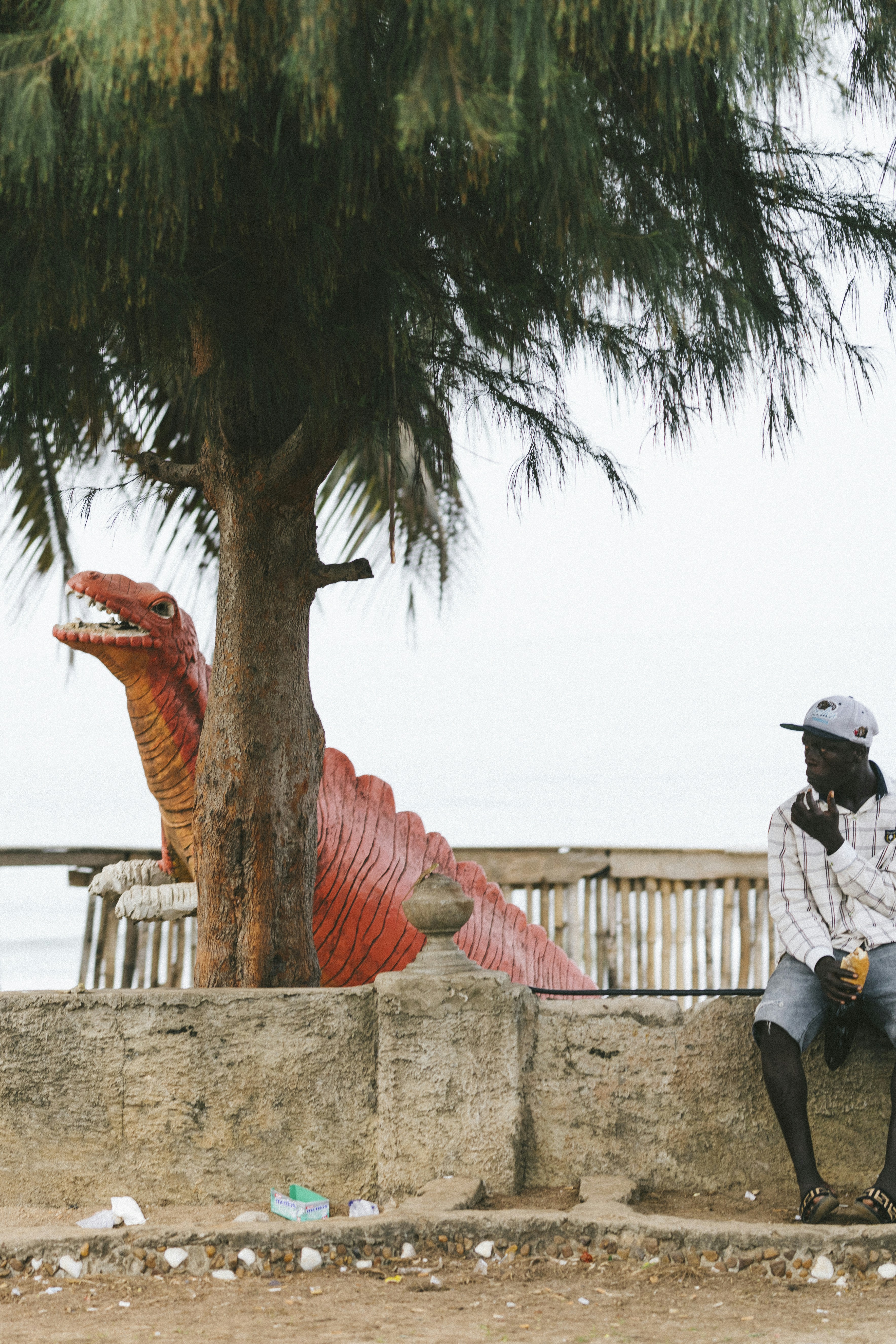 Street scene. Man waiting next to a dinosaurs on play ground in Freetown, Sierra Leone. Public sculpture. 