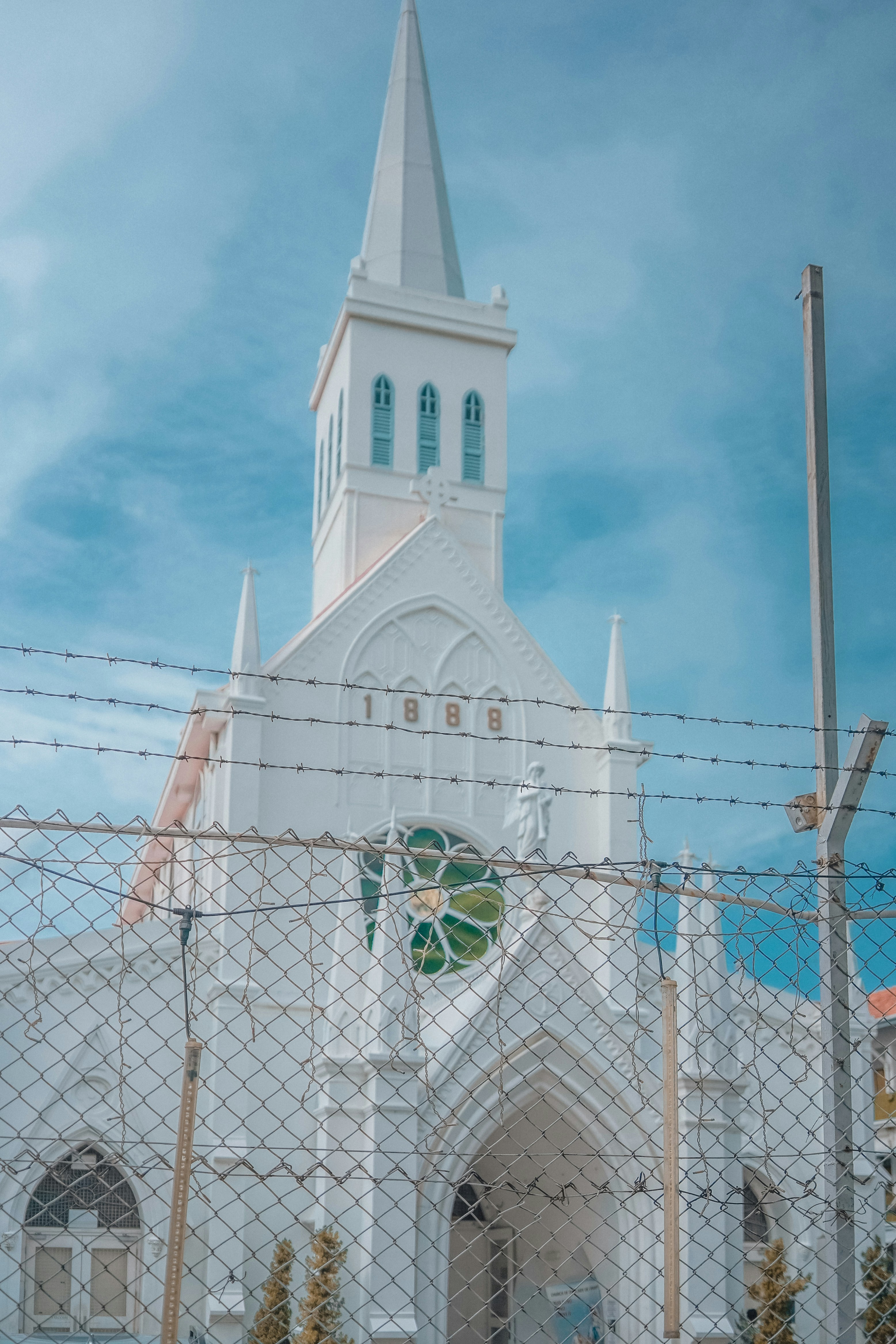 White Gothic Chapel Framed by Barbed Fence Under a Bright Azure Sky