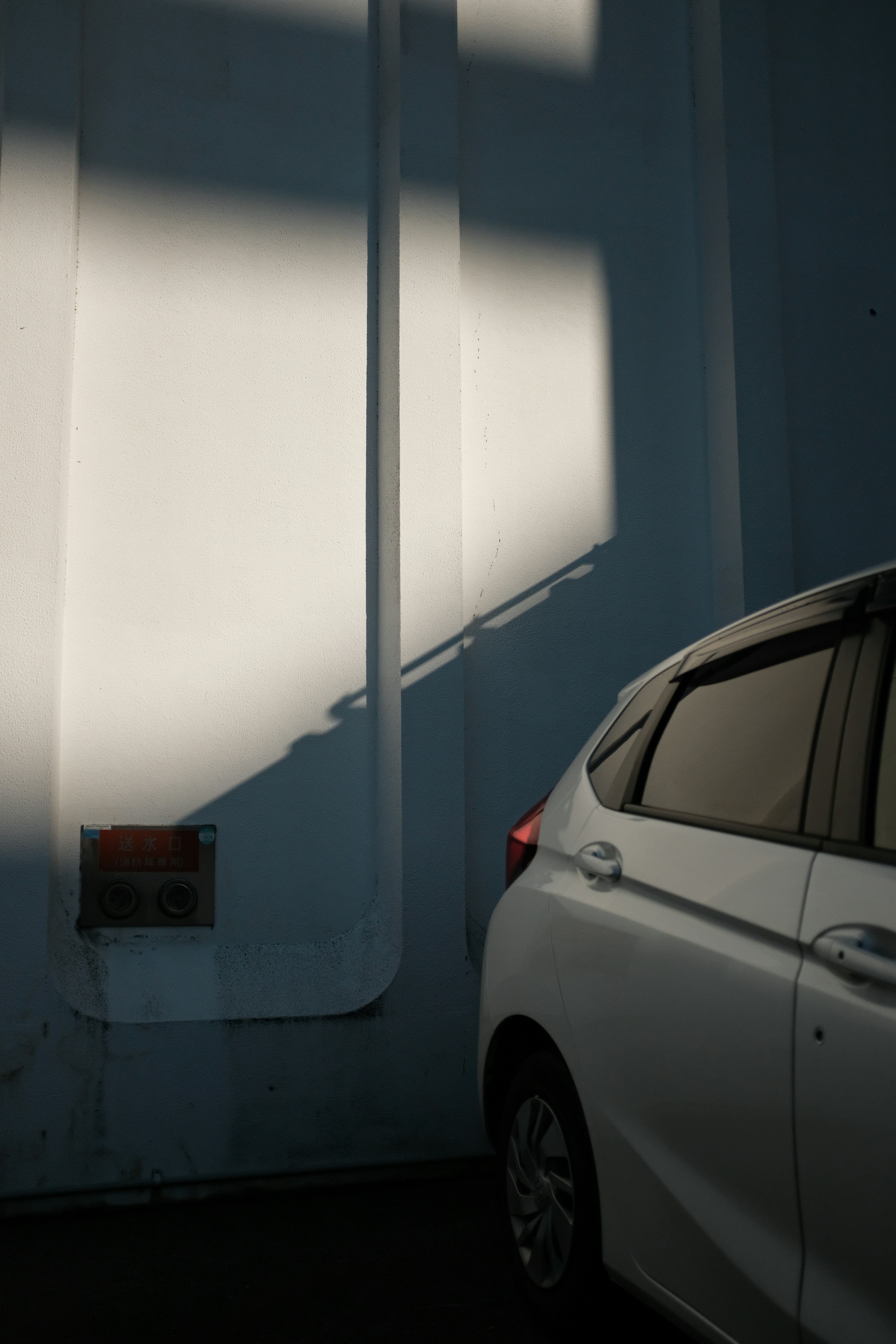 Diagonal Light on a White Hatchback by a Shadowed Blue Wall
