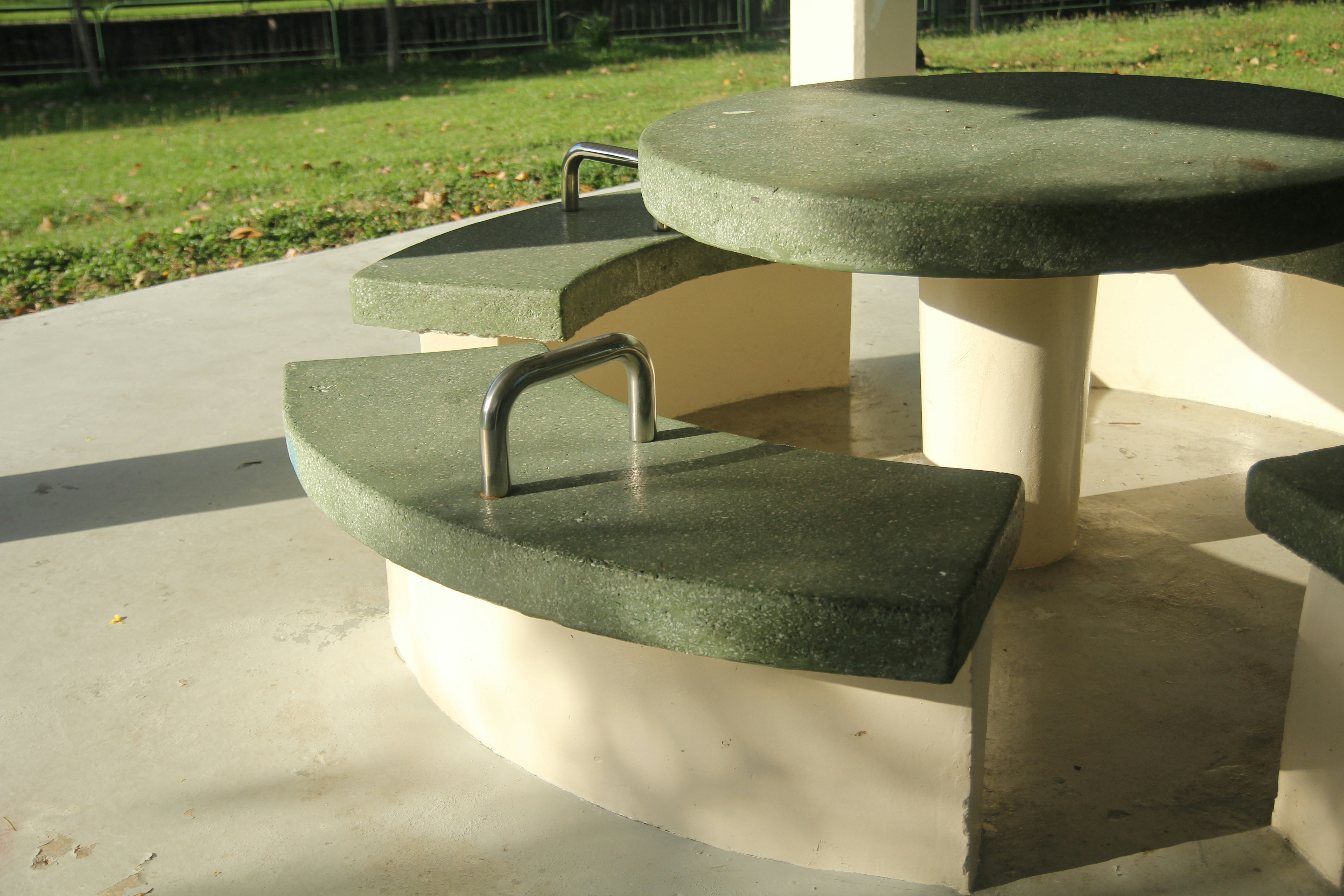Curved green stone benches with metallic handles in a tranquil outdoor setting, inviting relaxation. 