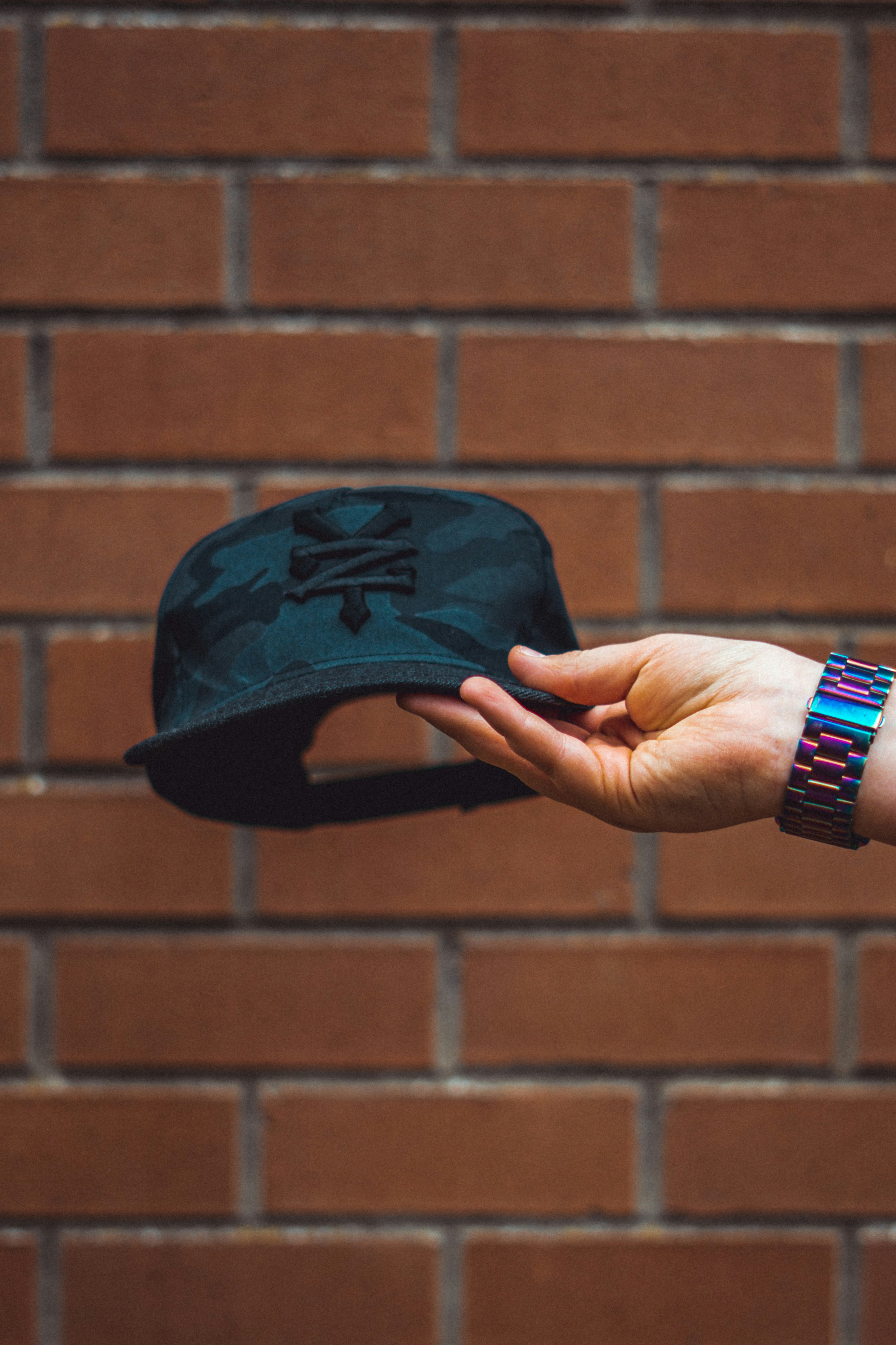 A Quiet Gesture: Camouflage Cap Suspended Before Brick Facade
