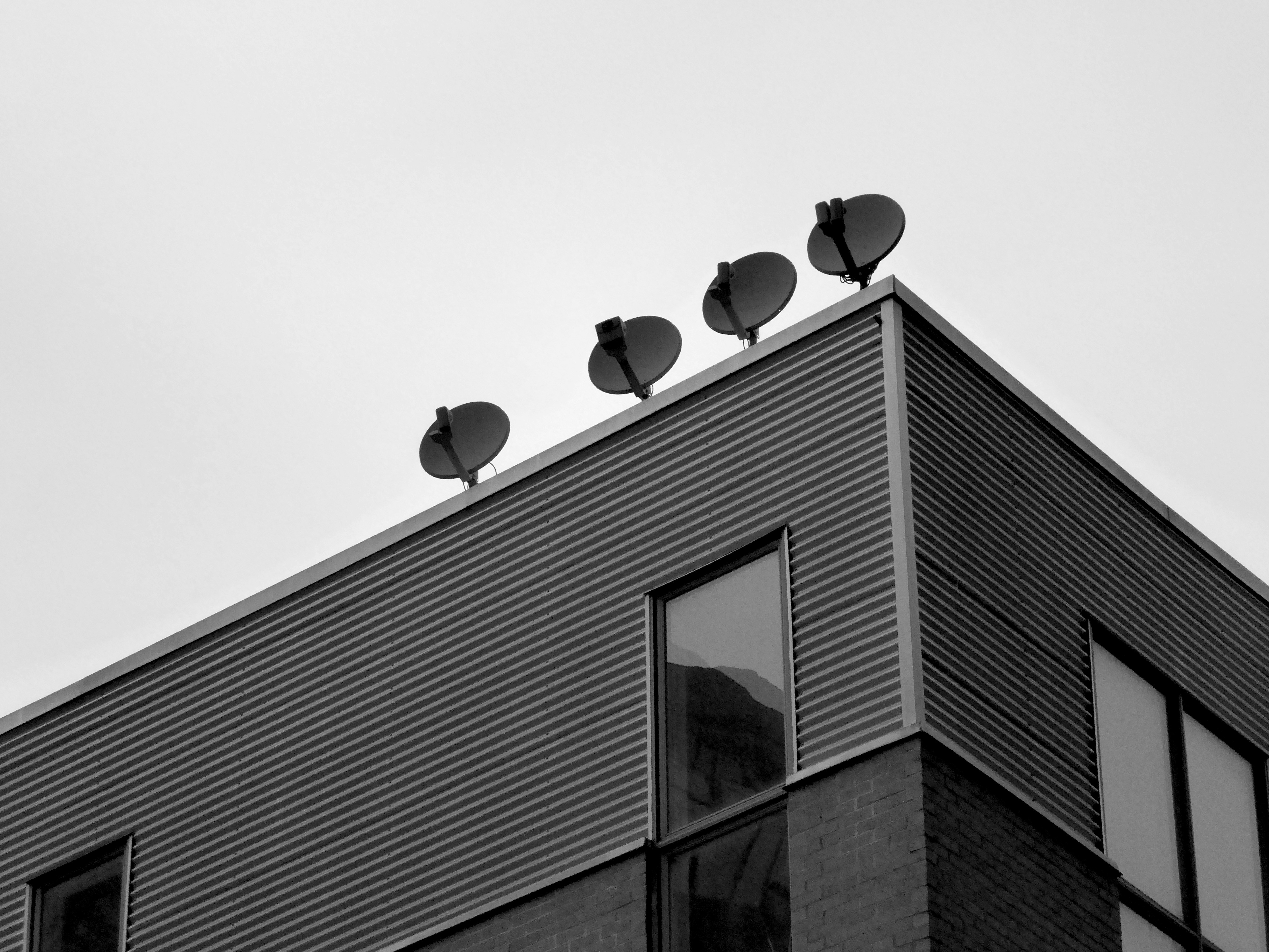 Satellite dishes perched on a modern building's rooftop against a cloudy sky.