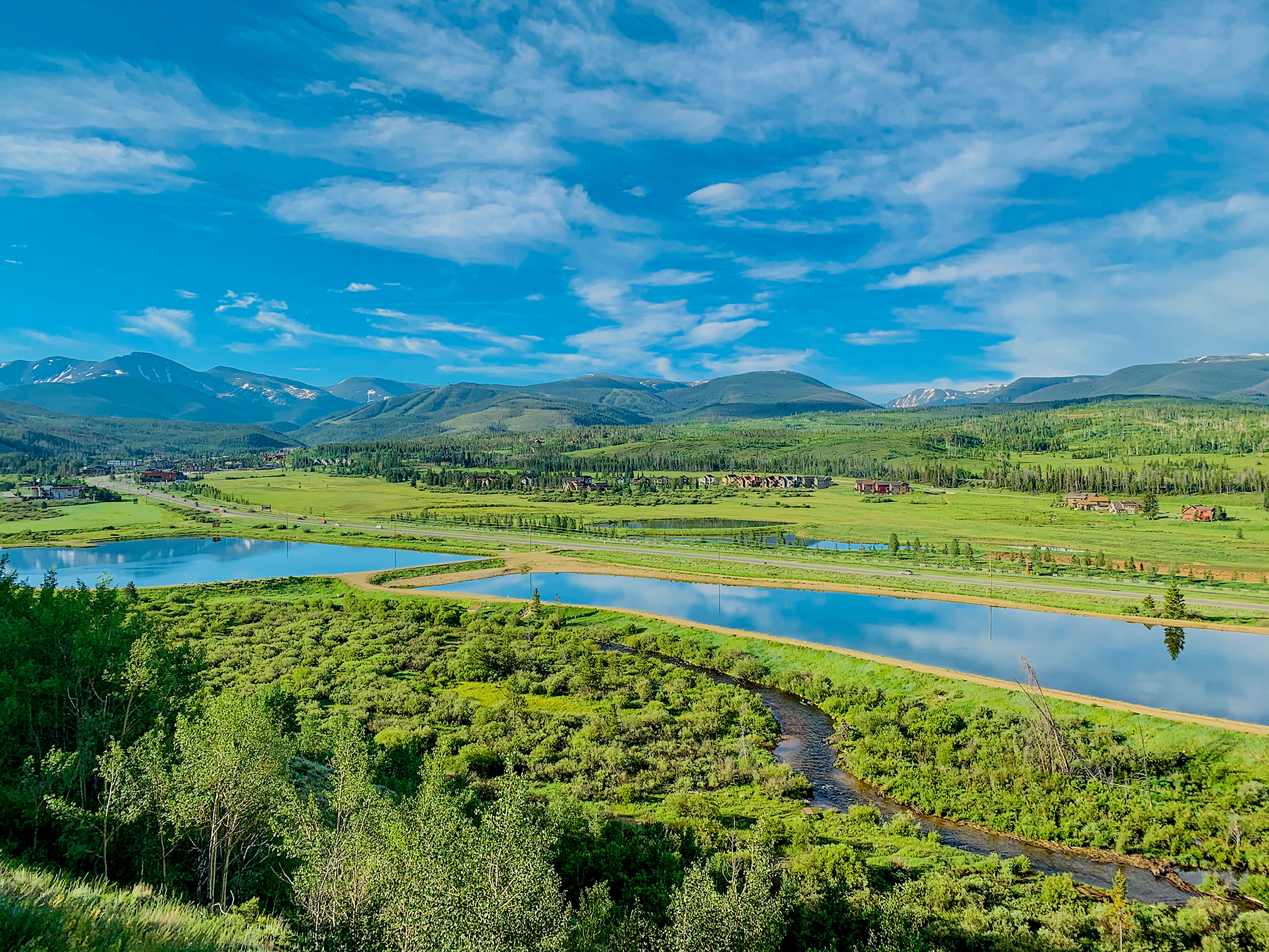 Lush green valleys interwoven with shimmering rivers under a clear blue sky, showcasing the beauty of untouched nature.