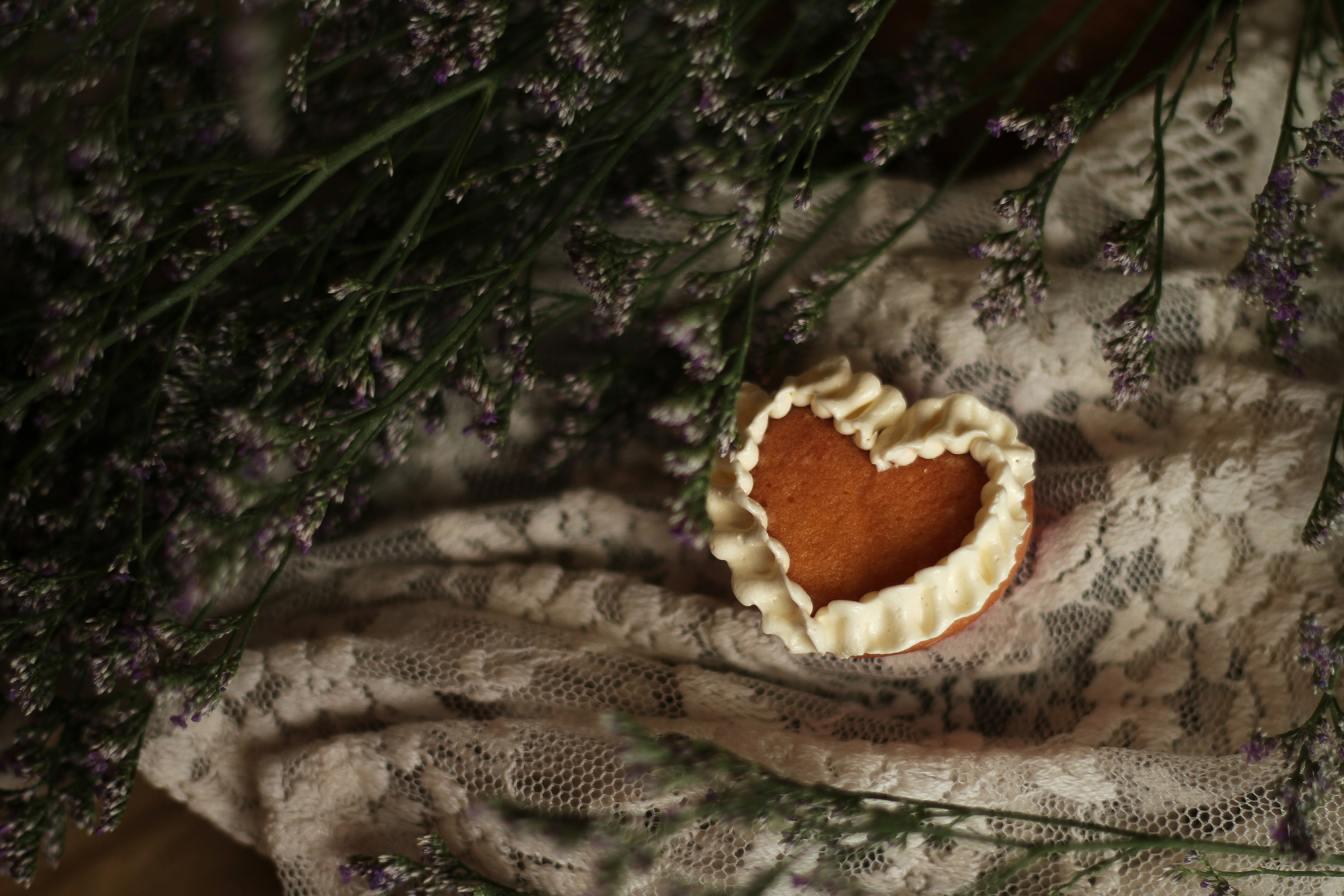 Heart-shaped dessert adorned with cream sits atop delicate lace, surrounded by lavender sprigs.