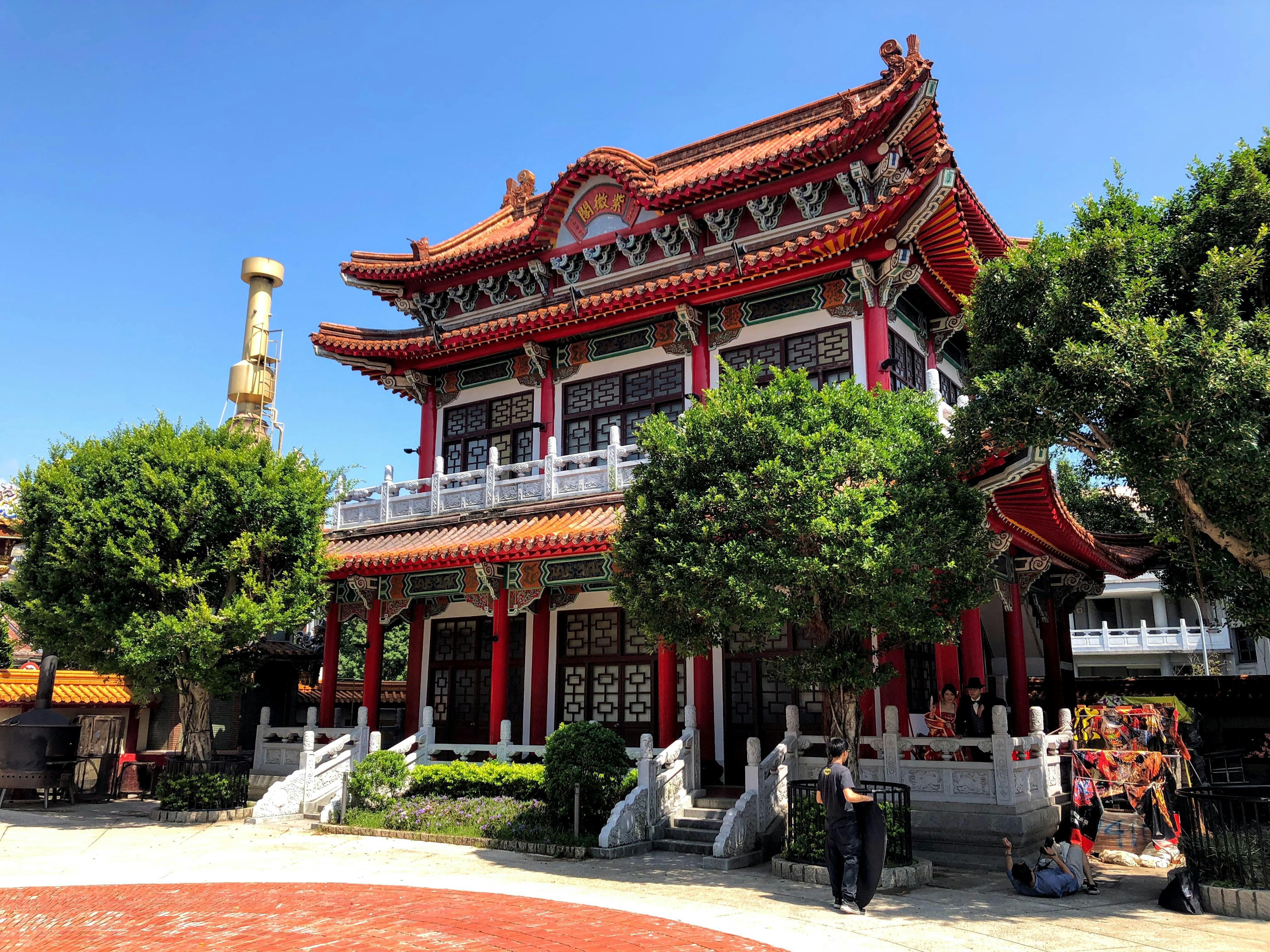 Traditional red-roofed pagoda surrounded by lush trees on a sunny day.