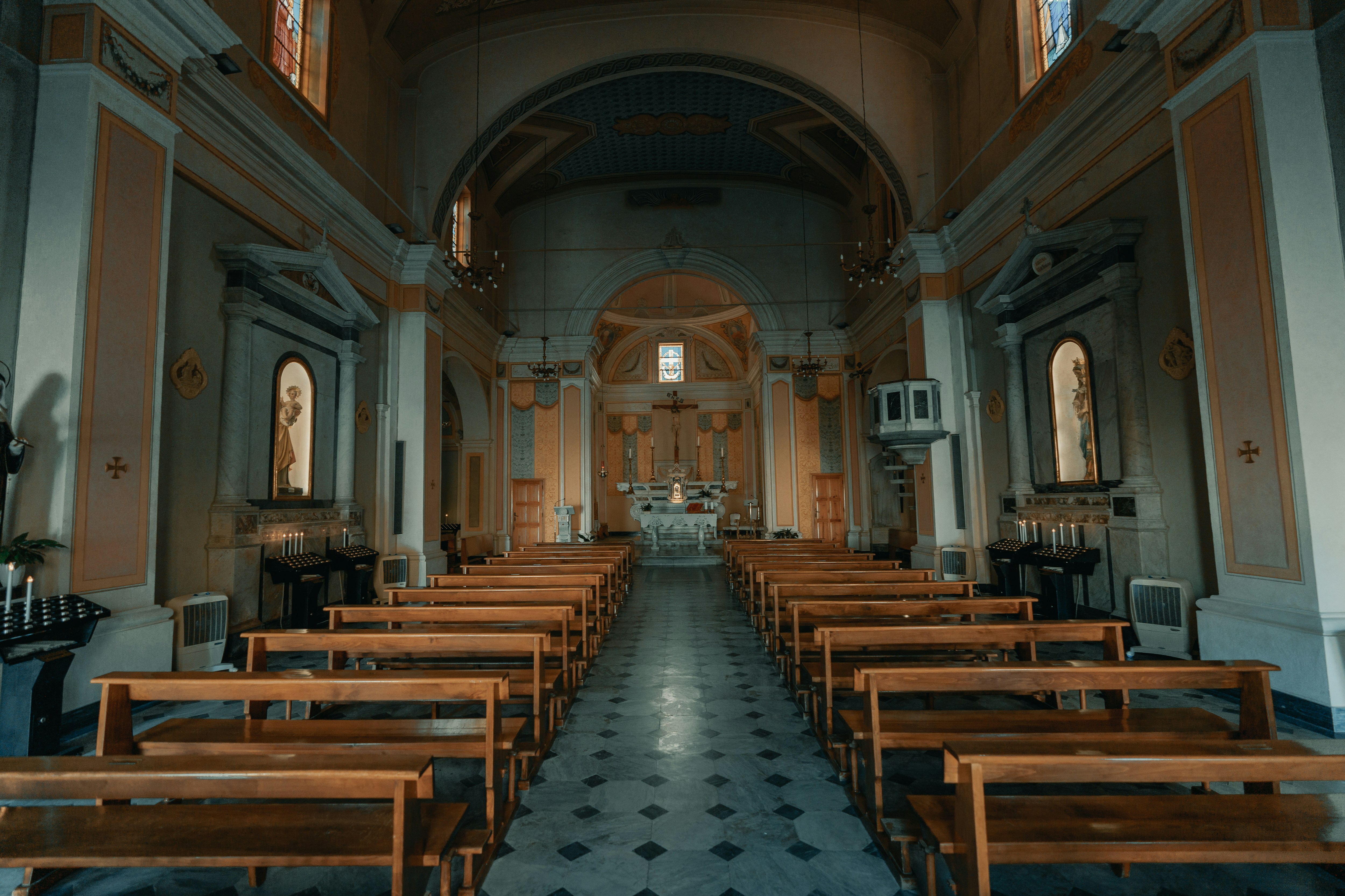 Interior of a church showcasing rows of wooden benches leading towards an altar adorned with religious figures.