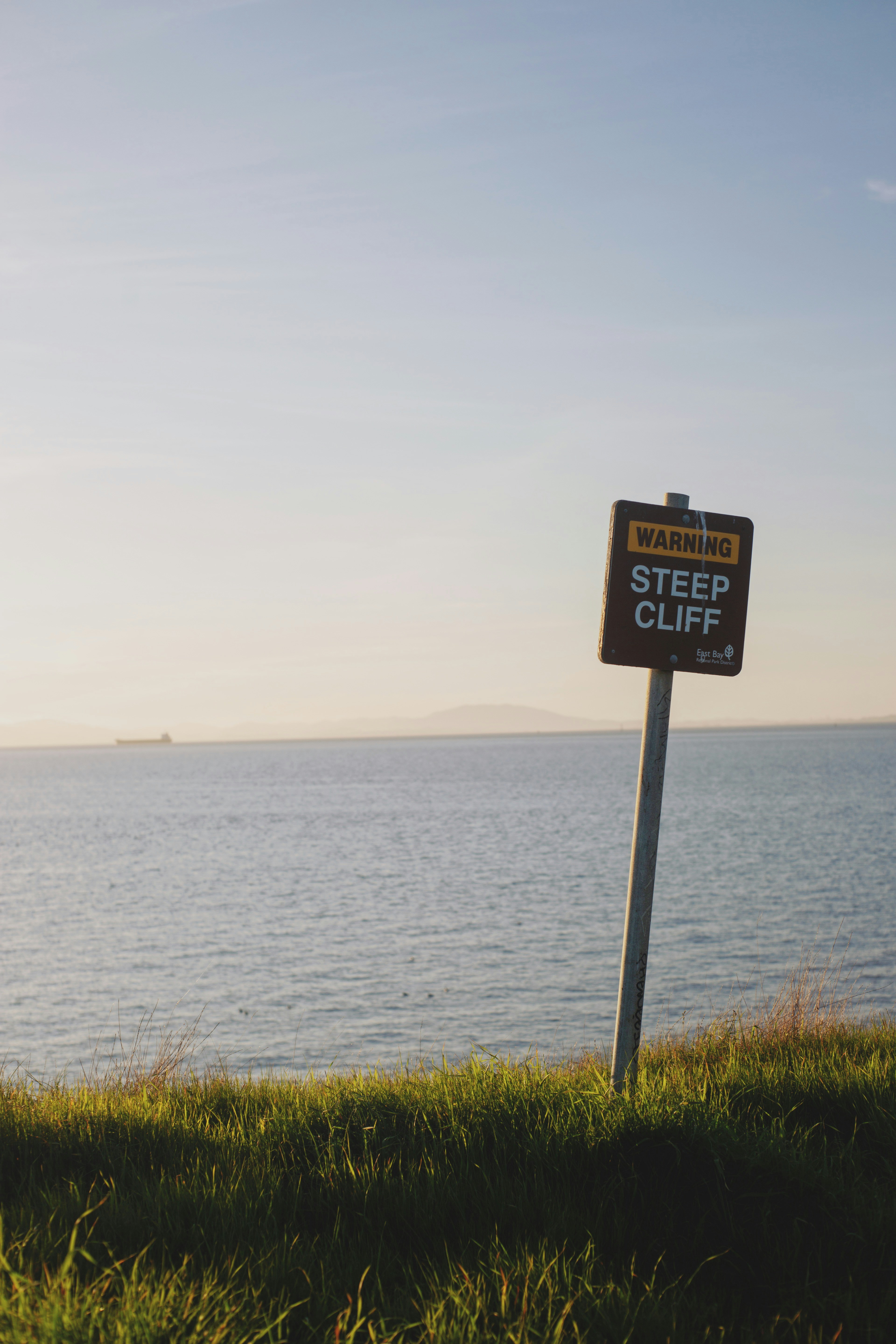Warning by the Waterfront: A Lone Sign Guards the Cliff Edge