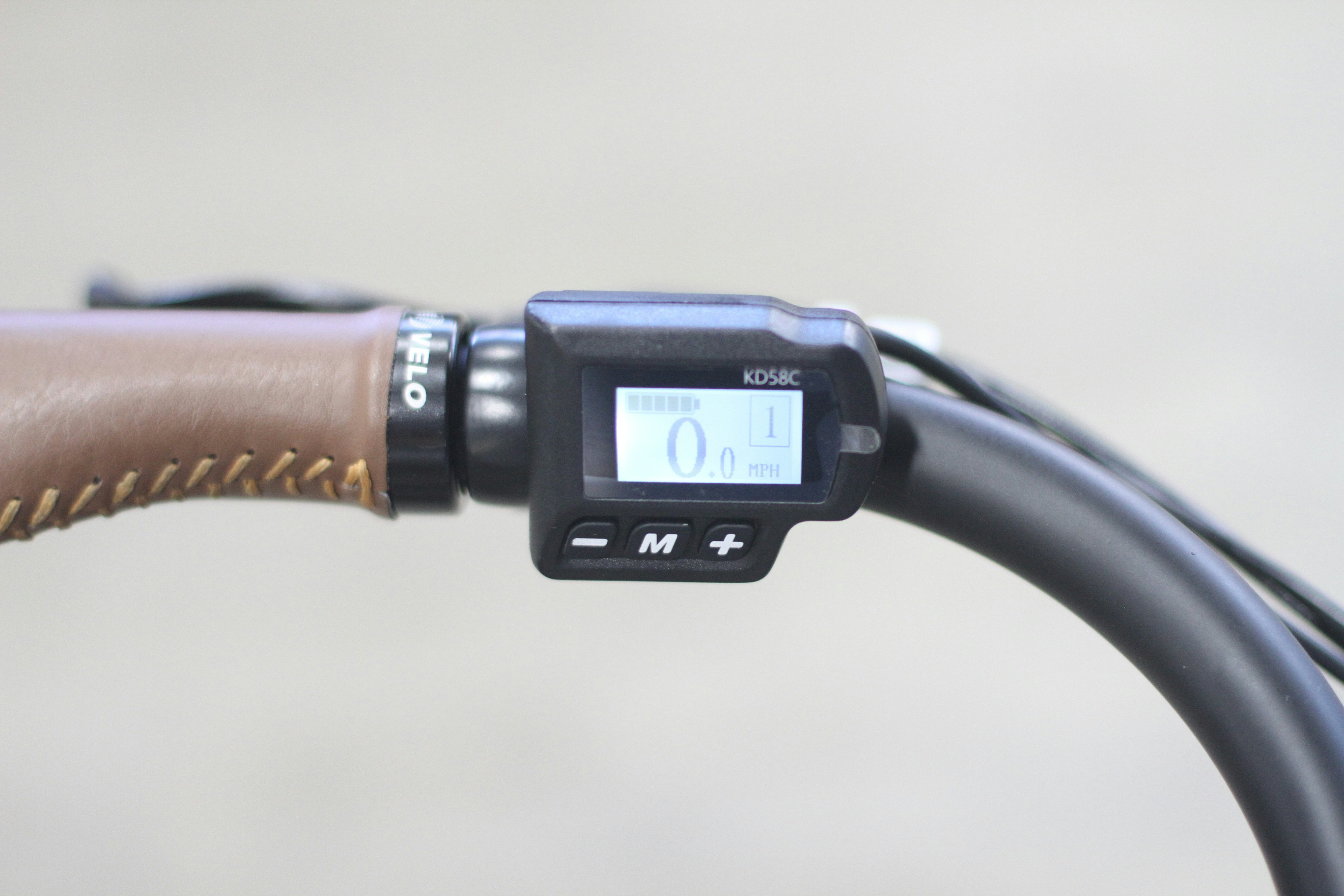 Digital speedometer mounted on a bicycle handlebar, displaying speed and distance metrics. The sleek design complements the leather grip of the handlebar.