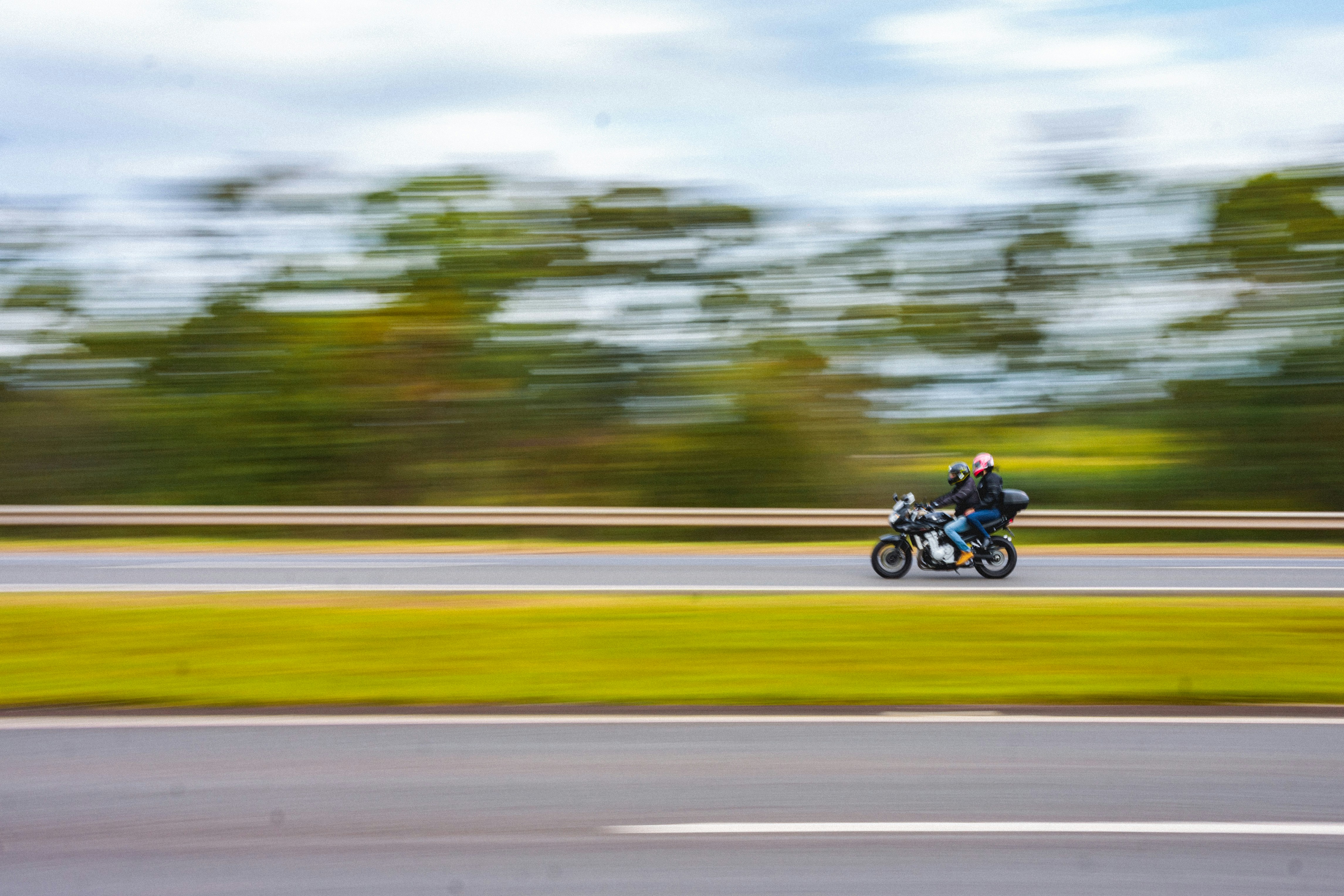 Motorcyclist zooming along a highway with a blurred background of greenery and sky.