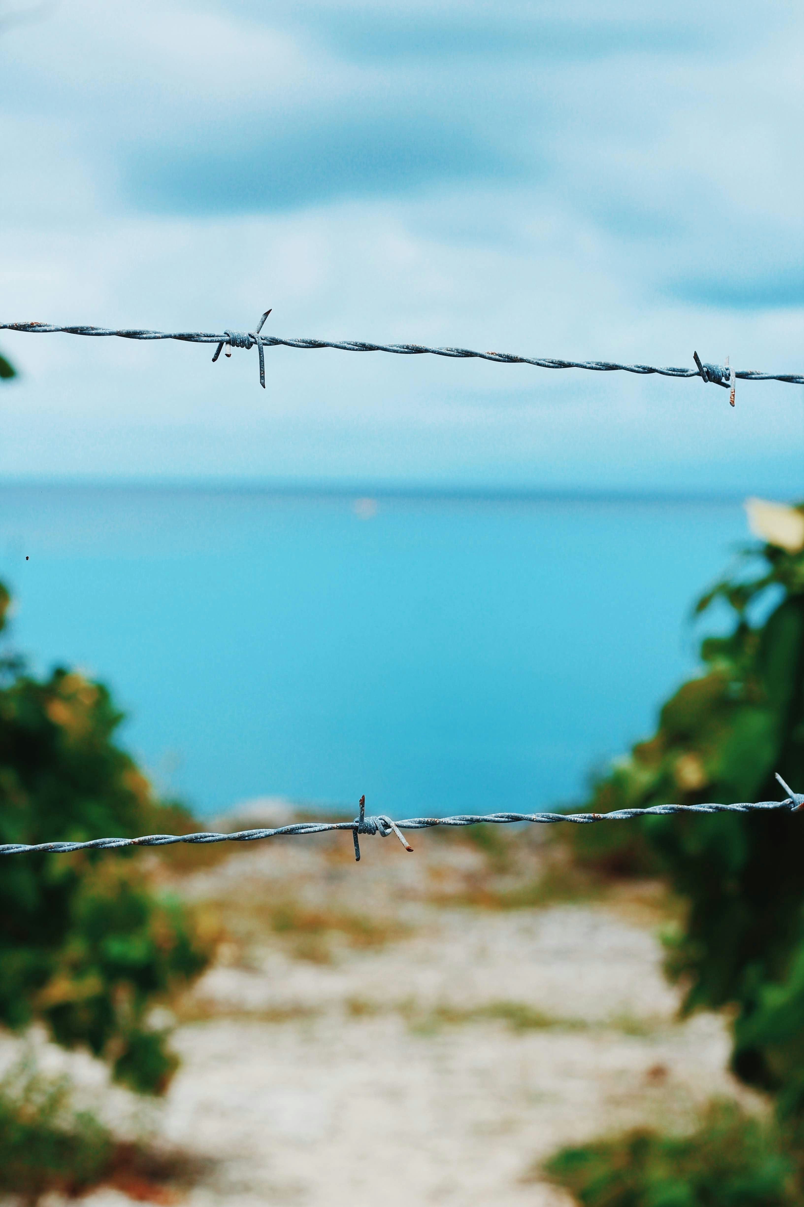 Barbed Horizon: Chain-link Silhouette Over a Turquoise Sea
