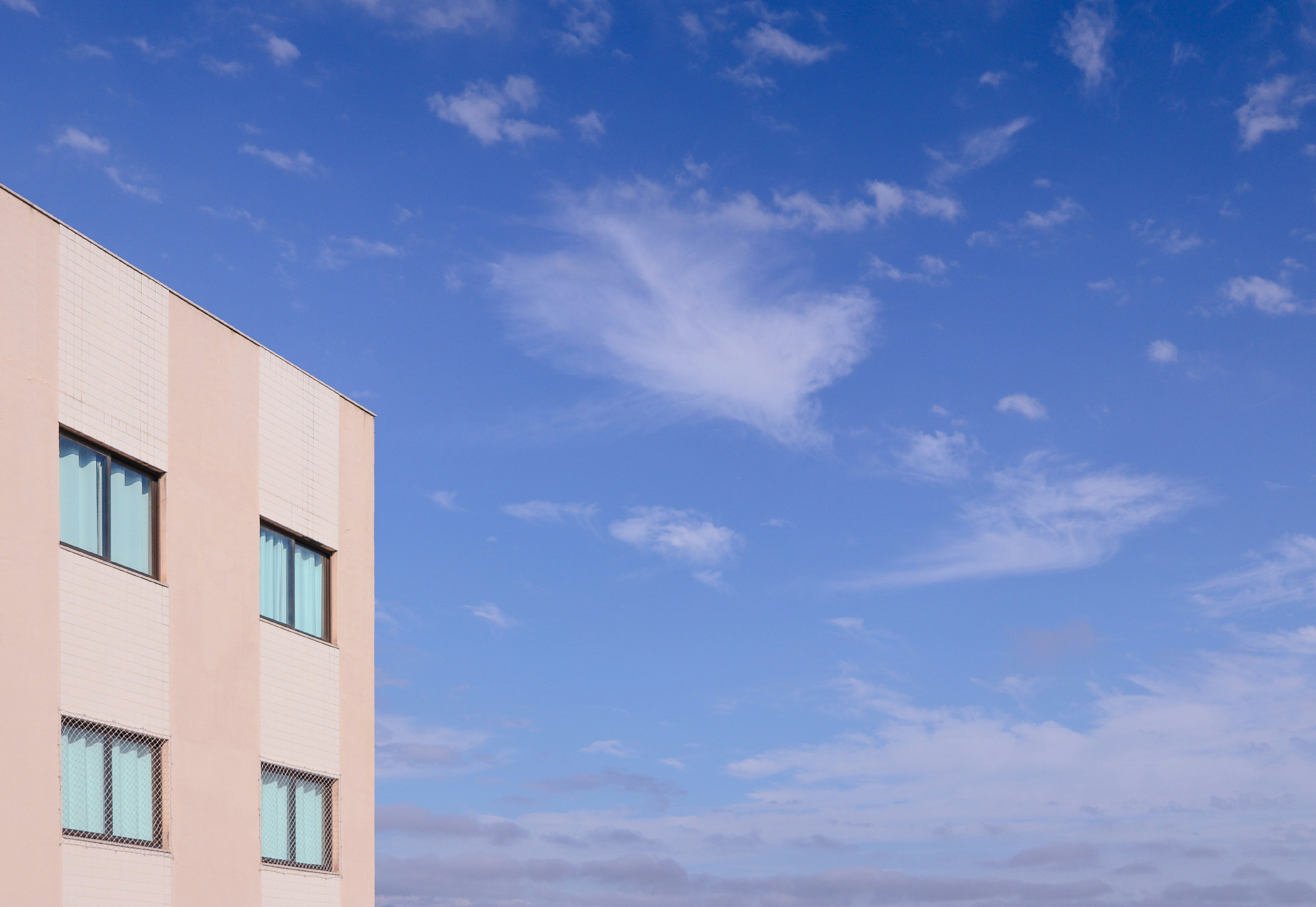 Modern building corner with large windows against a bright blue sky dotted with wispy clouds.